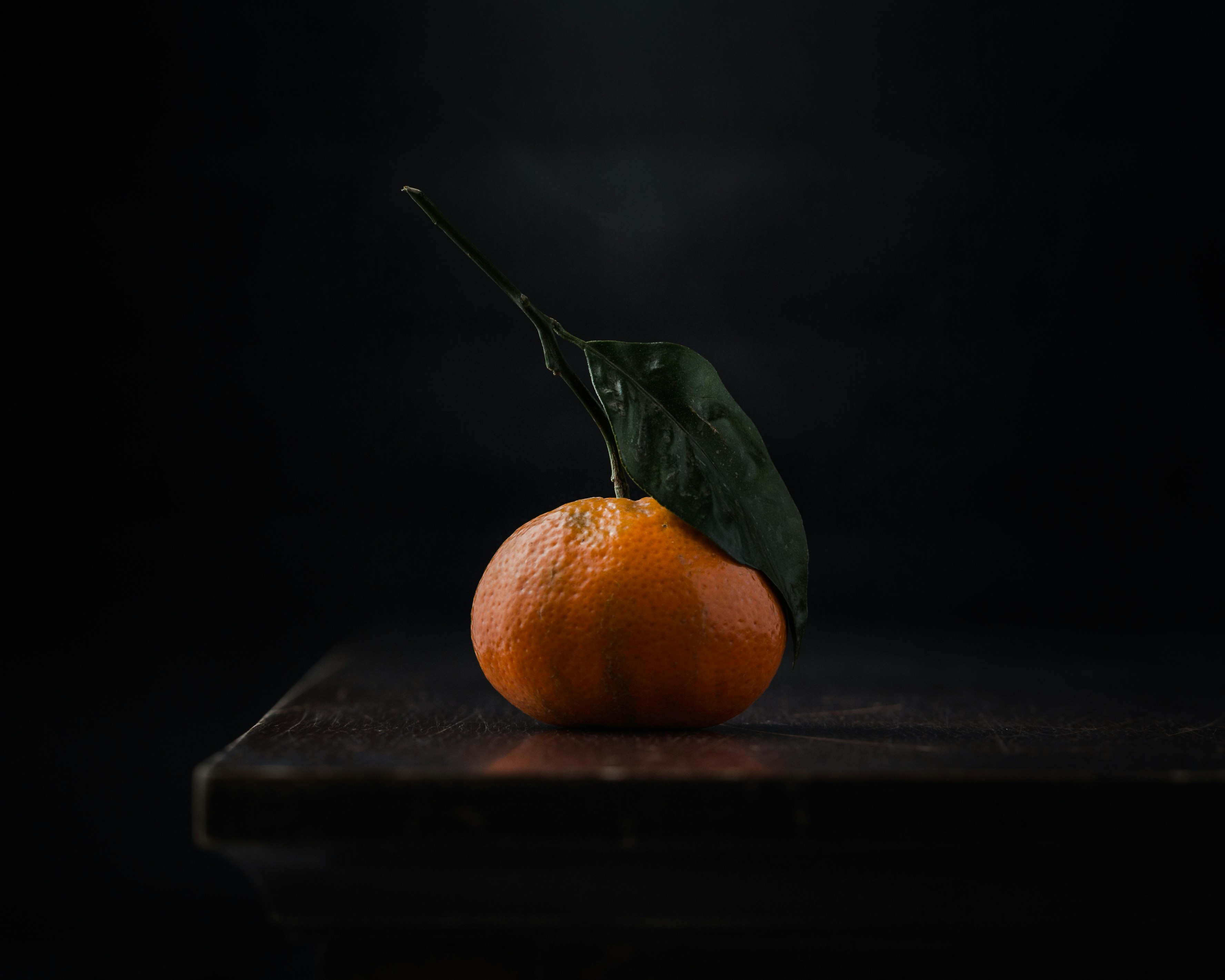 Mandarin orange with a green leaf on a dark wooden surface.