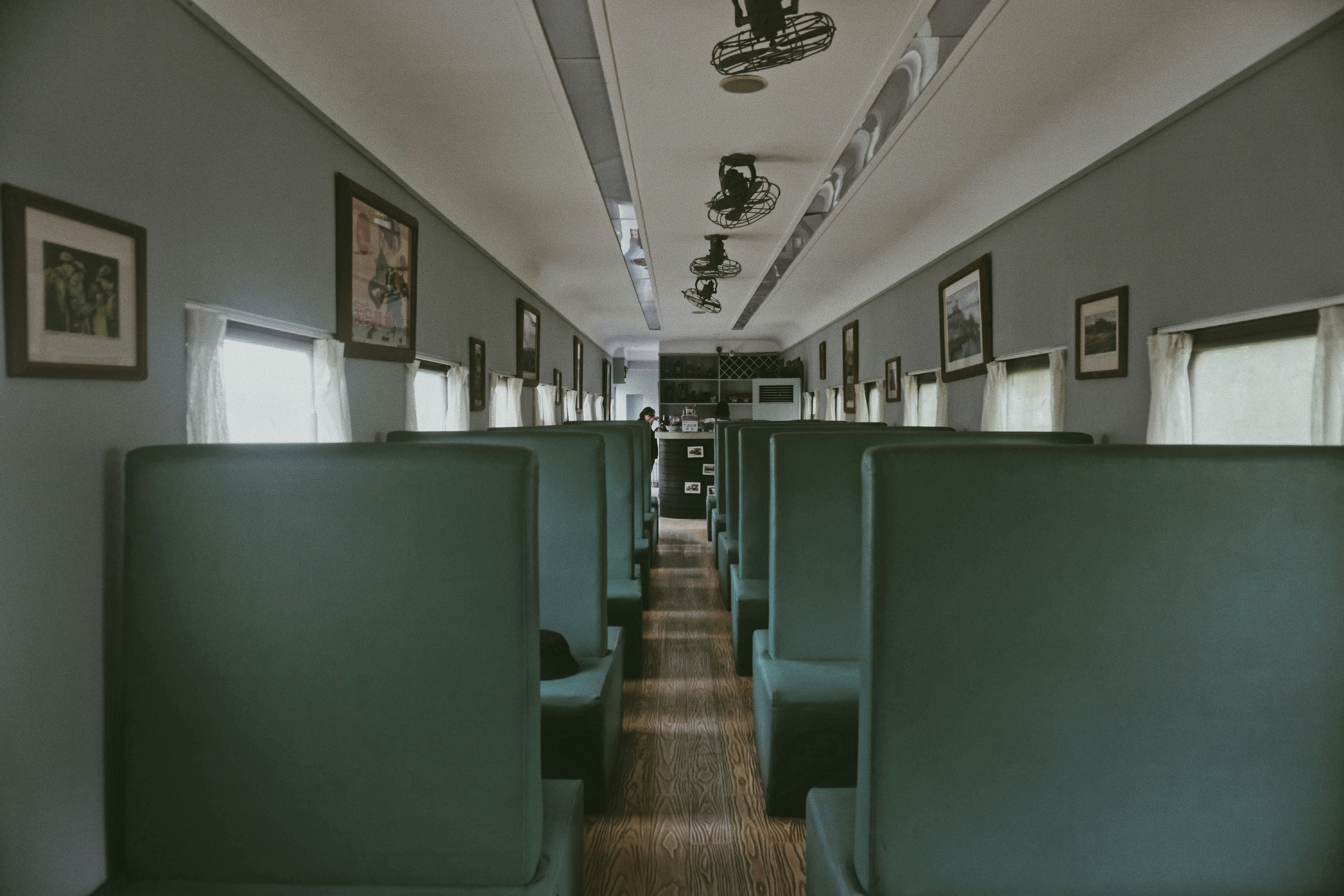 Interior view of a vintage train carriage featuring green seating and framed photographs on the walls.