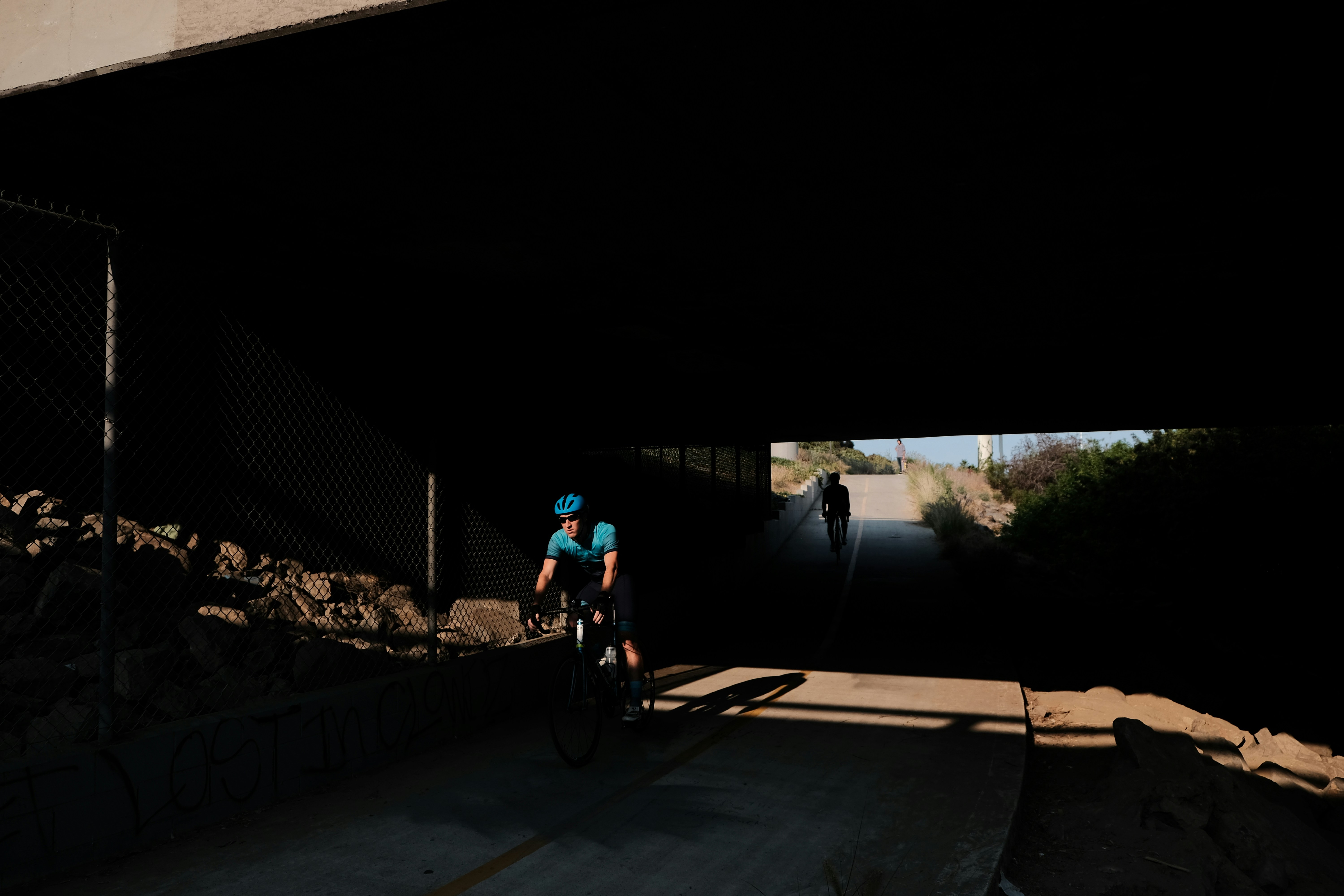 Emergence from Shadow: Turquoise Cyclist in a Quiet Underpass