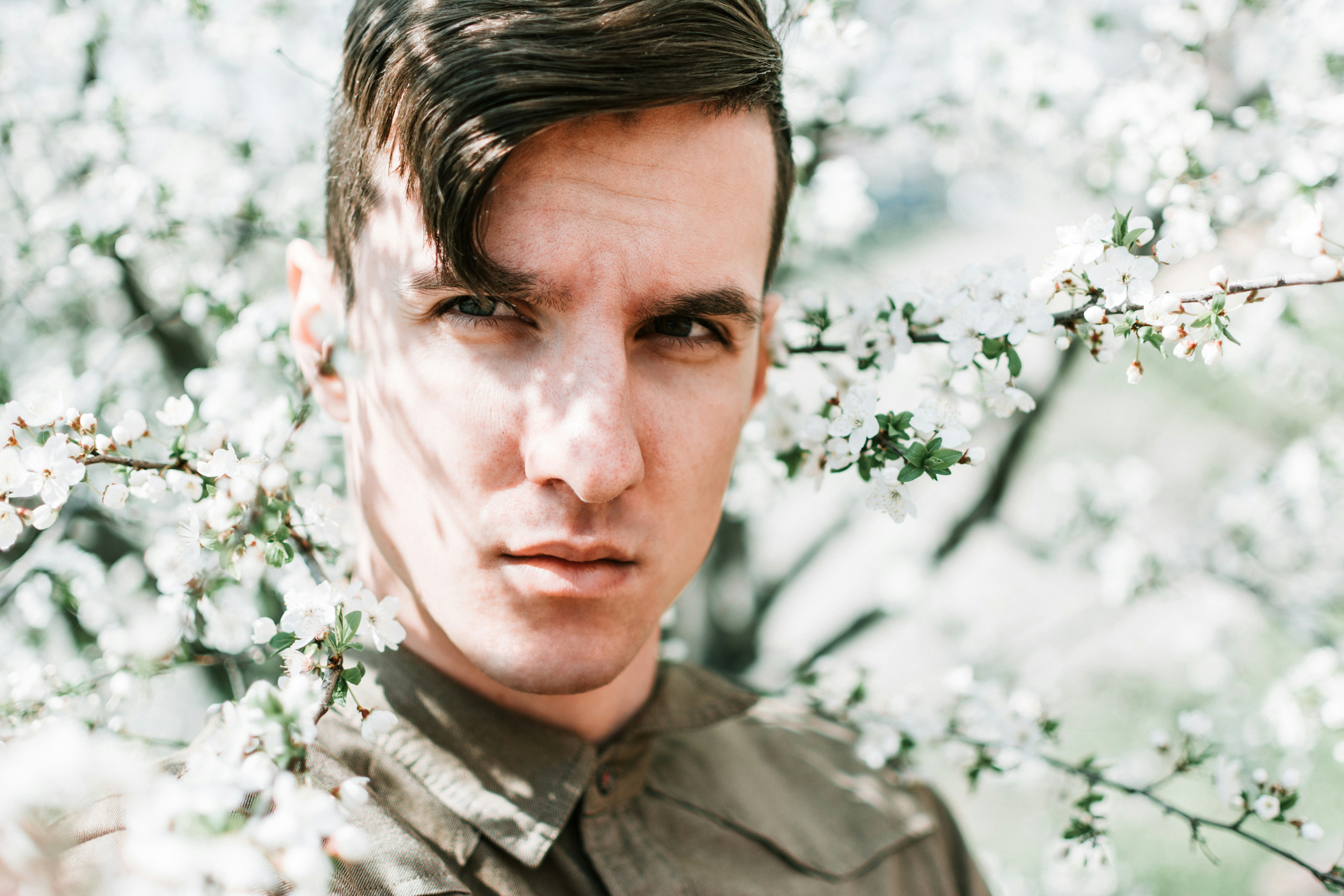 A young man gazes intently, framed by delicate white blossoms in full bloom. The soft lighting enhances the serene atmosphere.