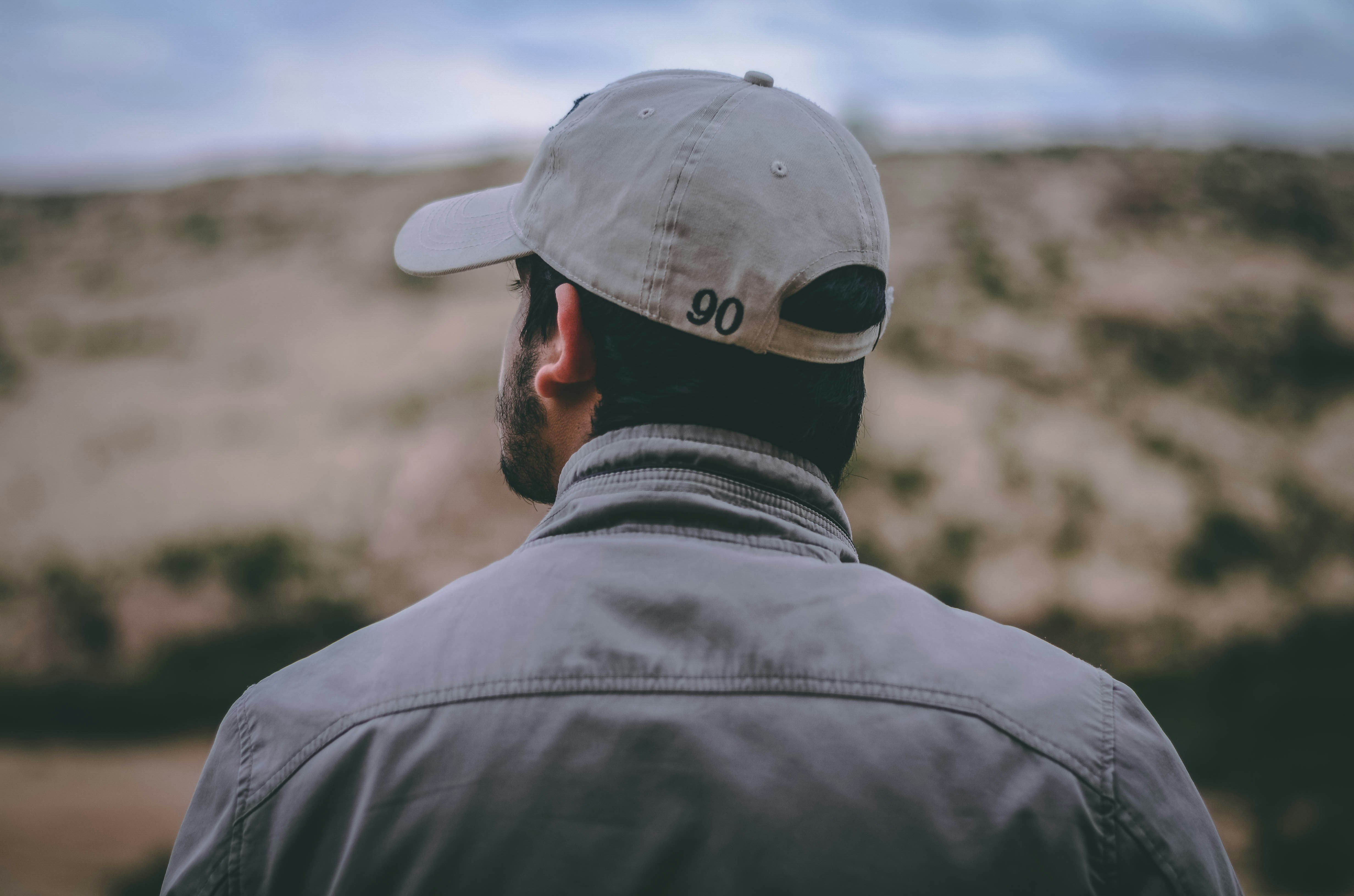 Man in gray jacket and gray fitted cap facing land mass photo – Free ...