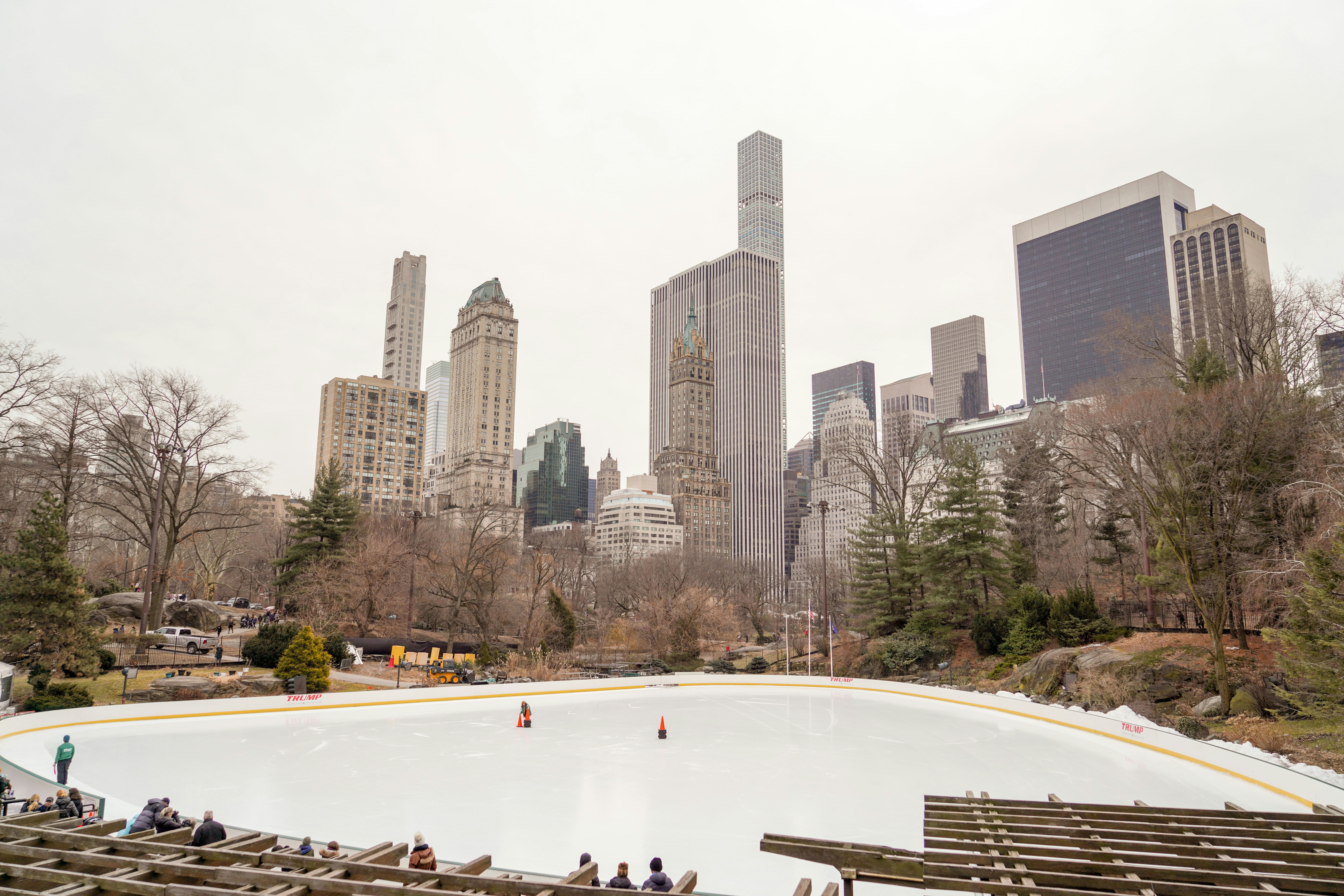 Ice skating rink nestled in a city park, surrounded by towering skyscrapers and winter trees. A serene winter scene showcasing urban life.