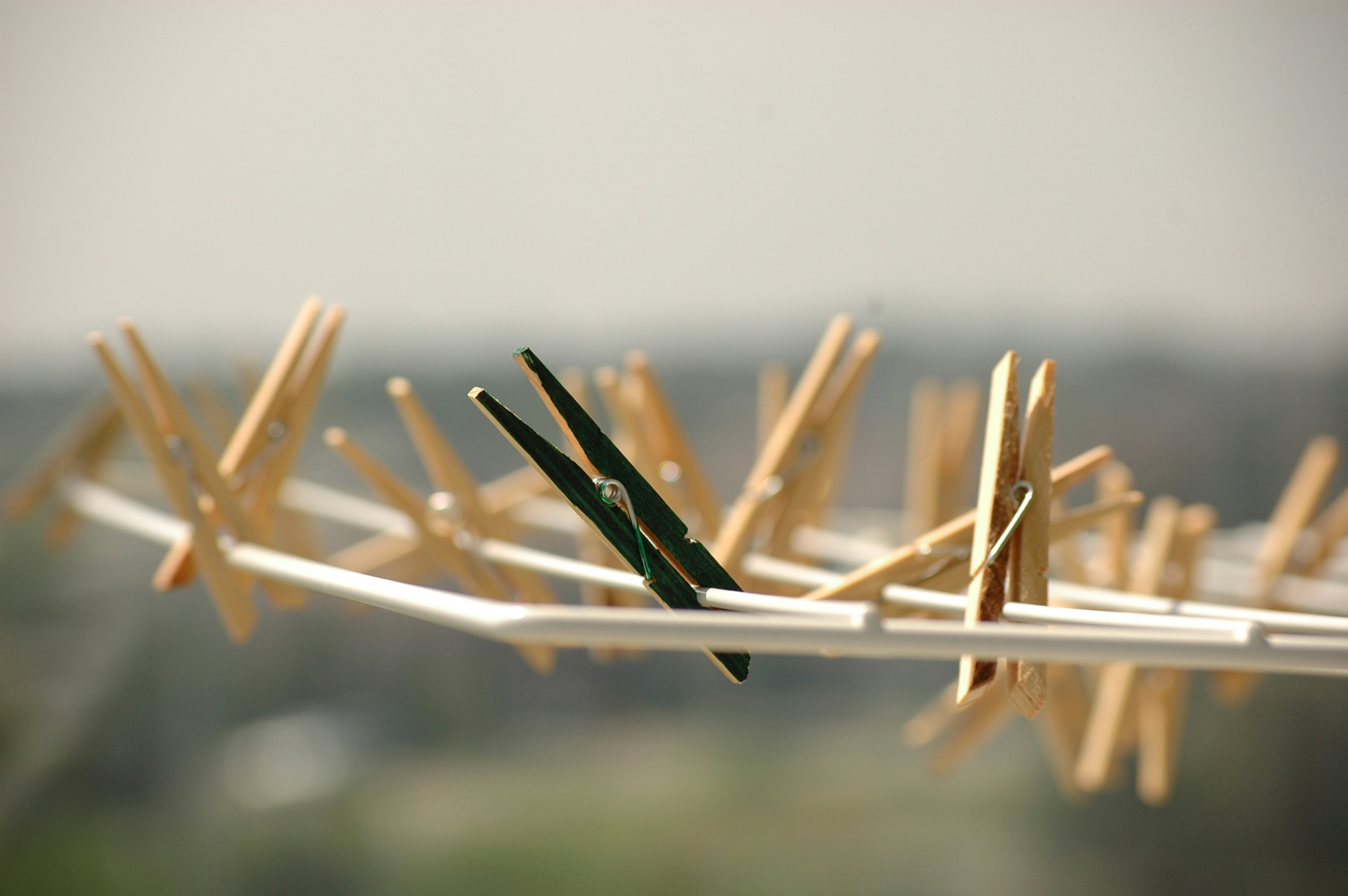 A single green clothespin stands out among wooden pins on a clothesline, with a shallow depth of field softening the background.
