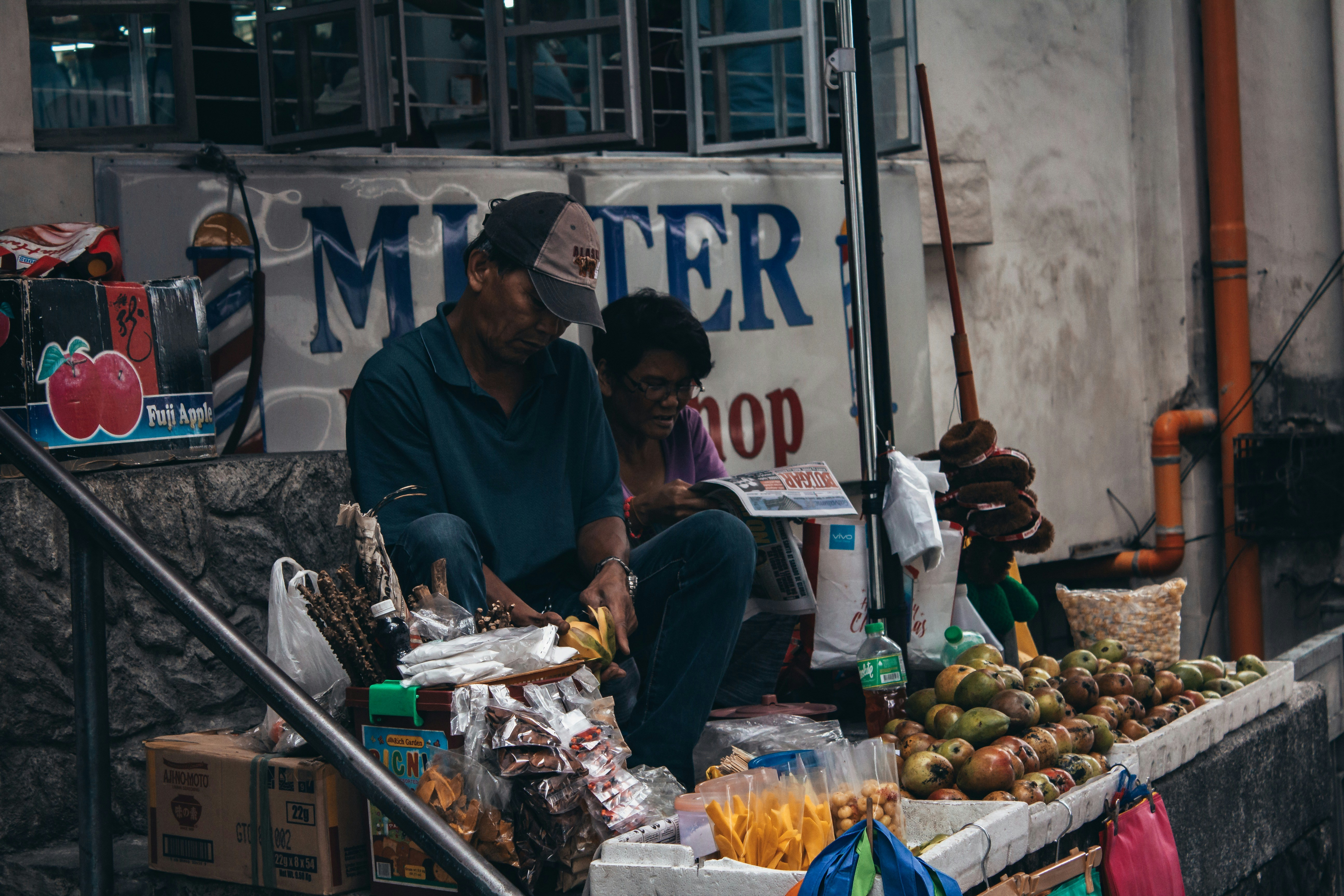 Vendors sell fruits and snacks on a bustling city street corner.