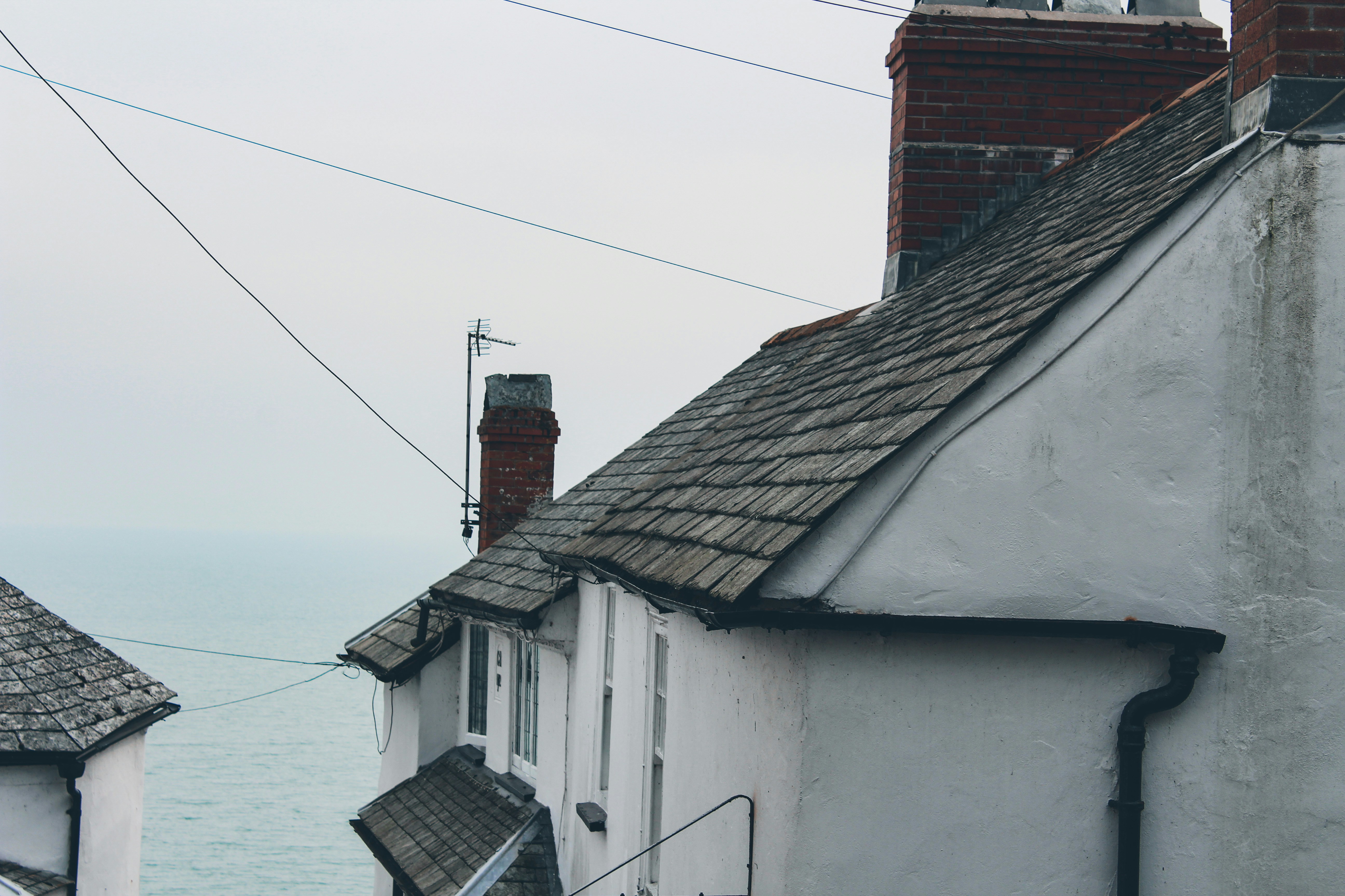 Weathered rooftops of coastal houses meet a tranquil sea backdrop under a soft, overcast sky.