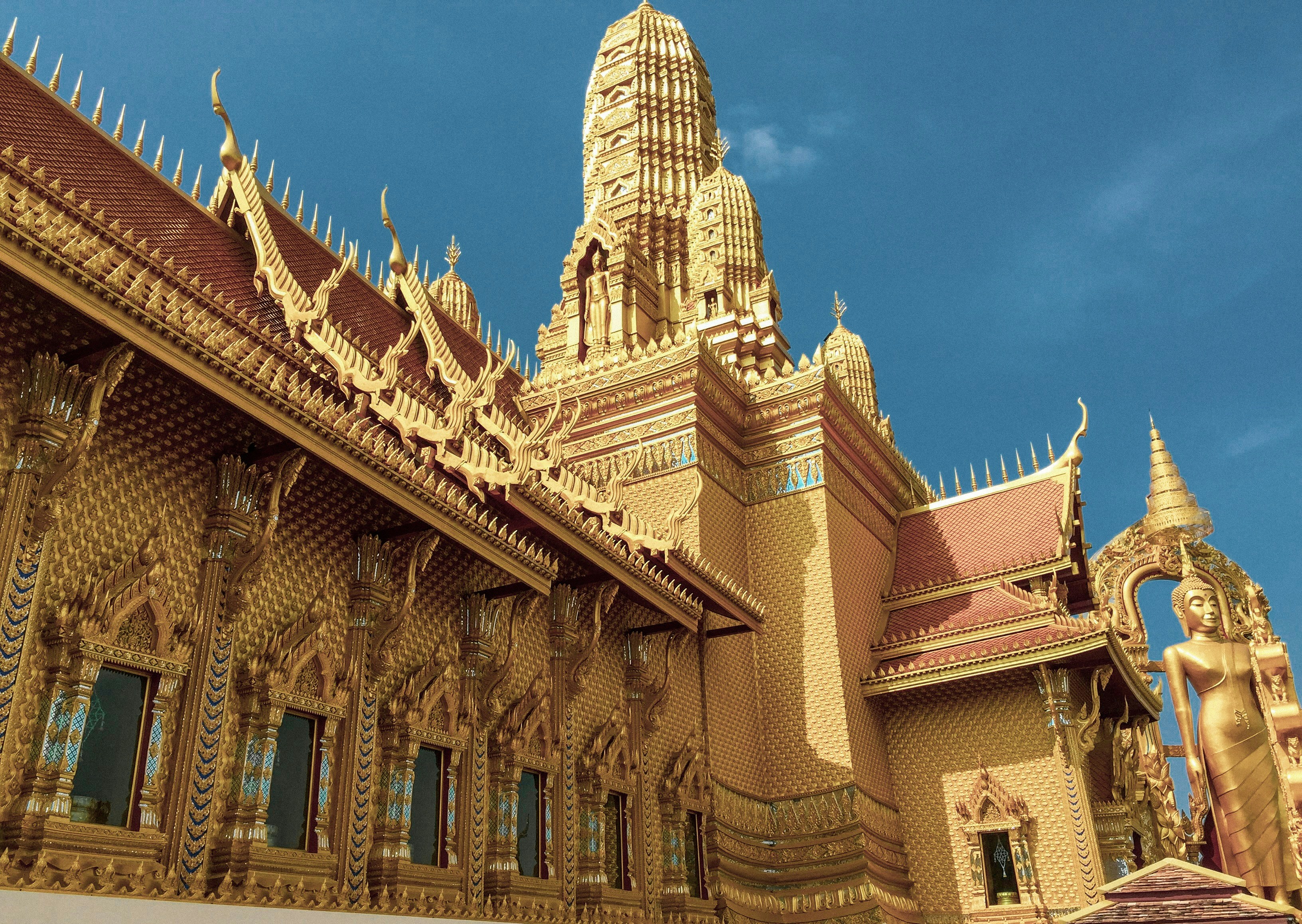 Intricate golden temple architecture showcasing ornate details and a serene Buddha statue in the foreground.