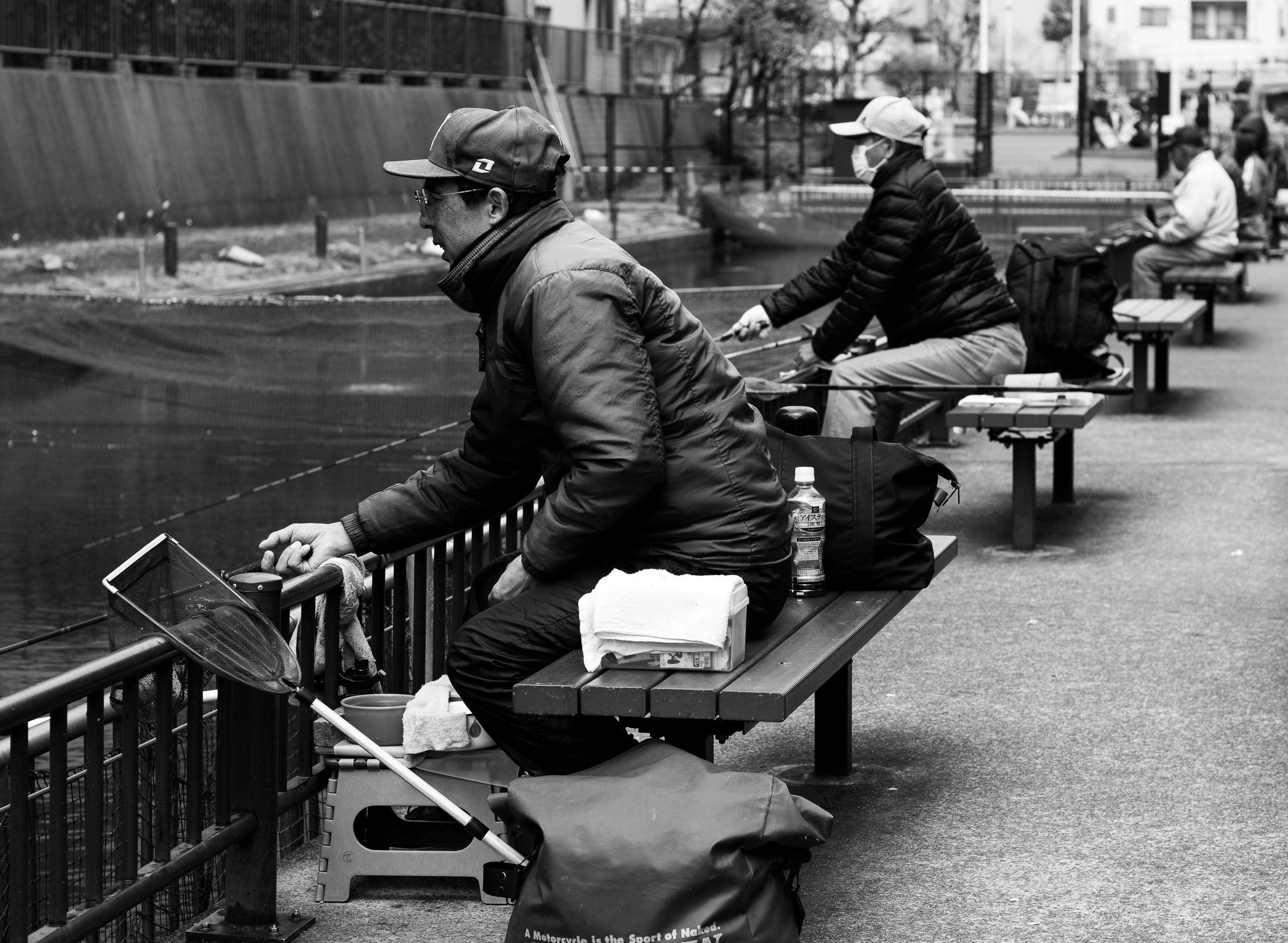 Benchside Anglers: Quiet Focus on a Riverbank in Monochrome