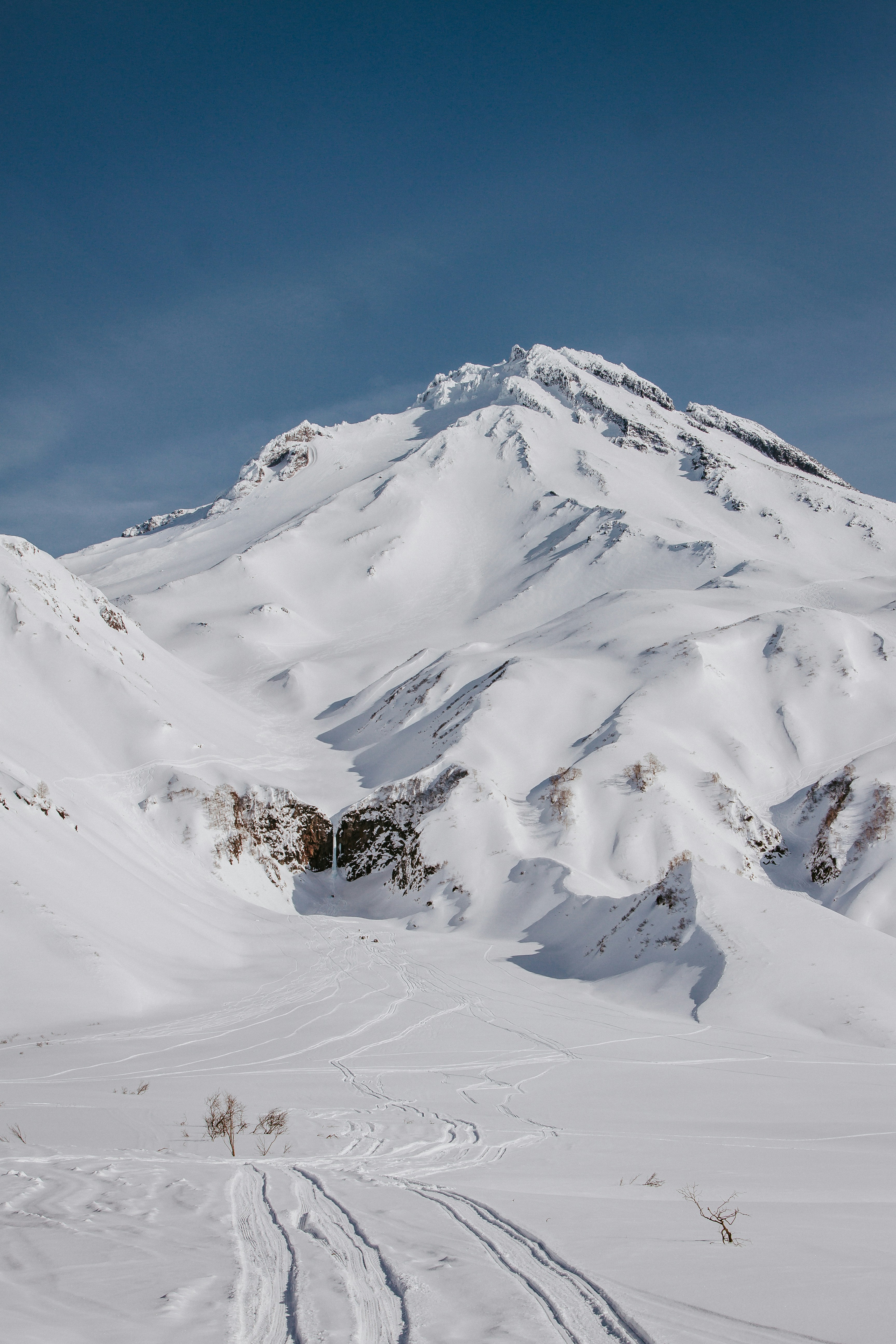Snow-covered mountains rise majestically against a clear blue sky, with trails etched in the pristine surface below.