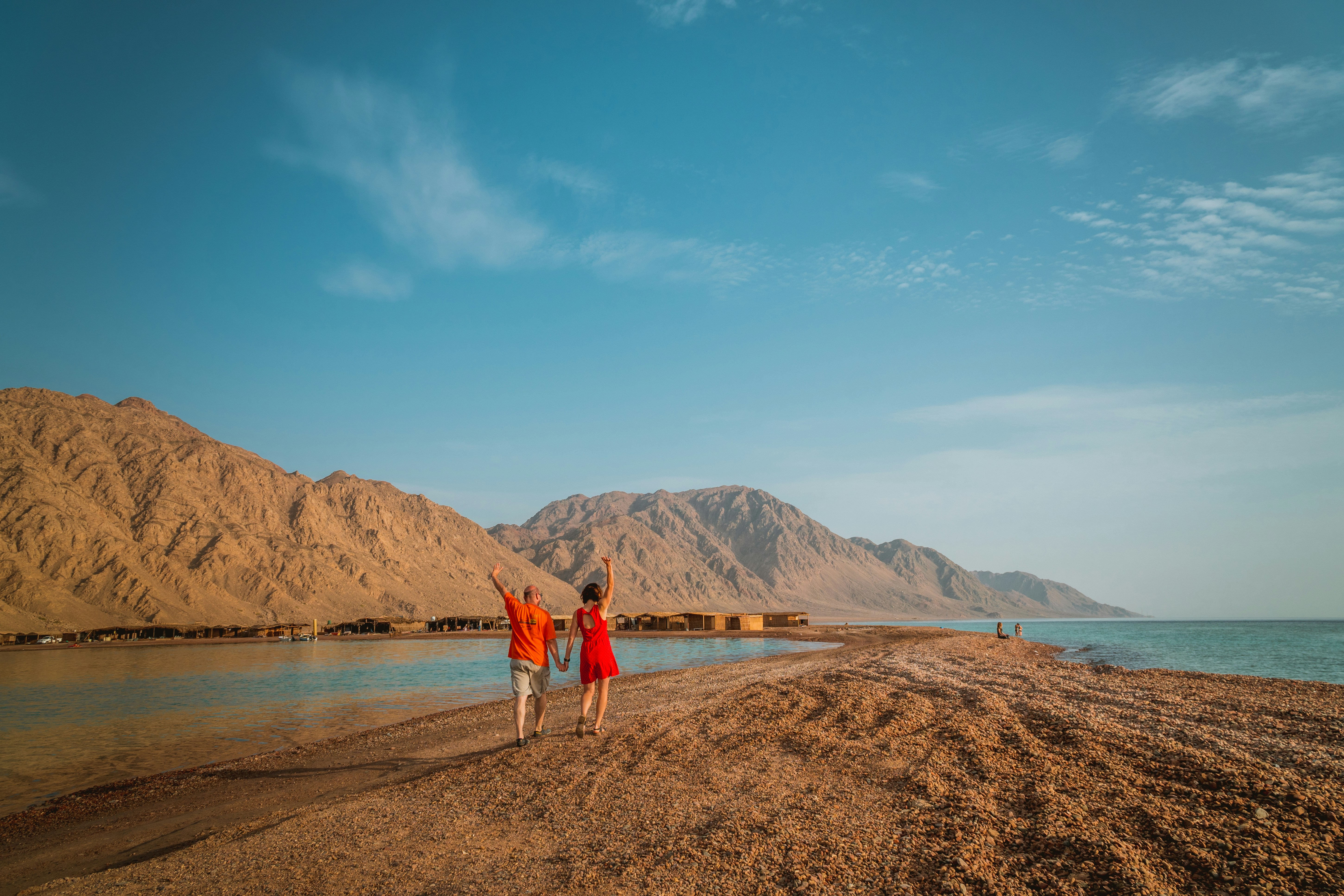 Red-Clad Pair Reaching for the Horizon on a Mountain-Backed Seaside