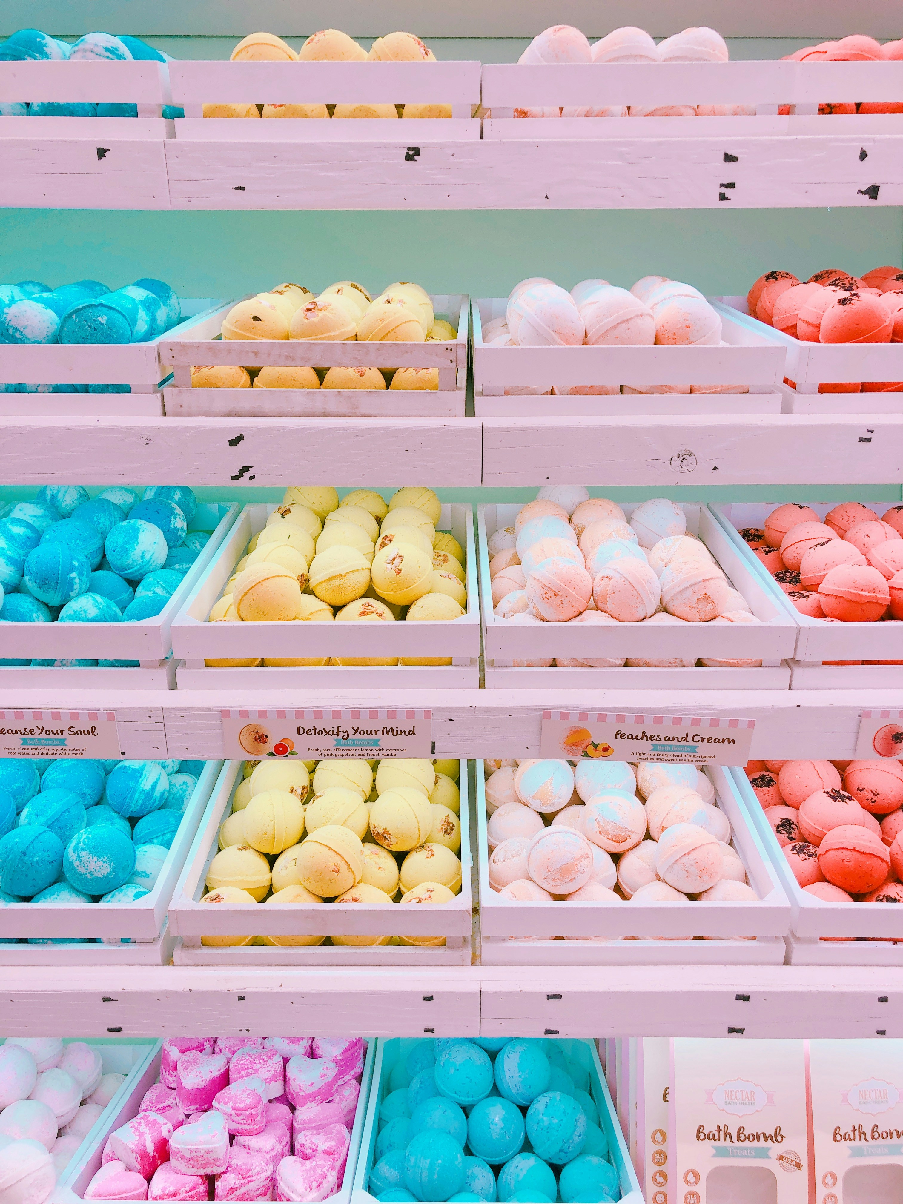 Vibrant assortment of bath bombs arranged in wooden trays, showcasing a spectrum of colors and textures. Each section labeled for easy selection.