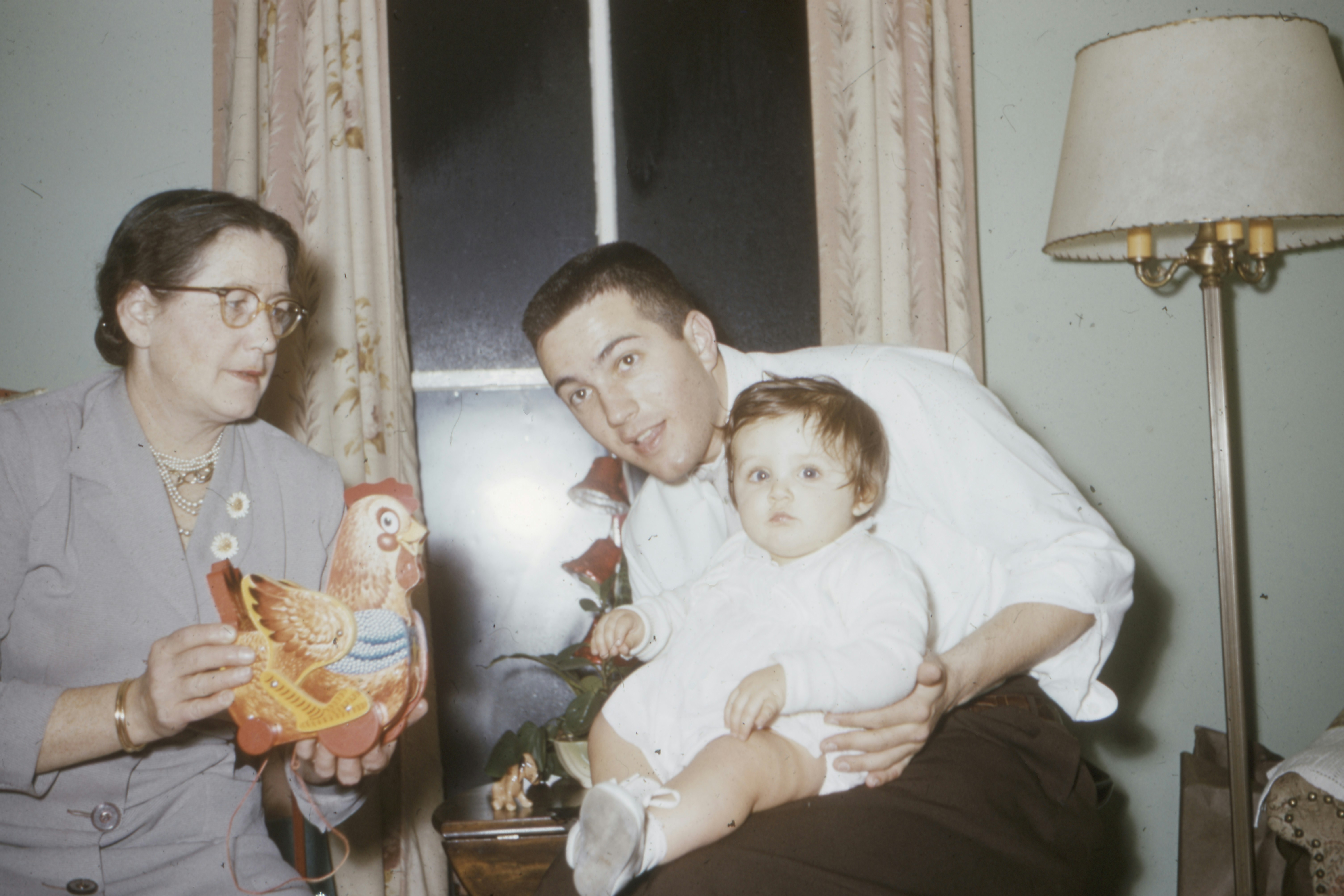 Three people gathered around a toy chicken near a window, capturing a nostalgic family scene.