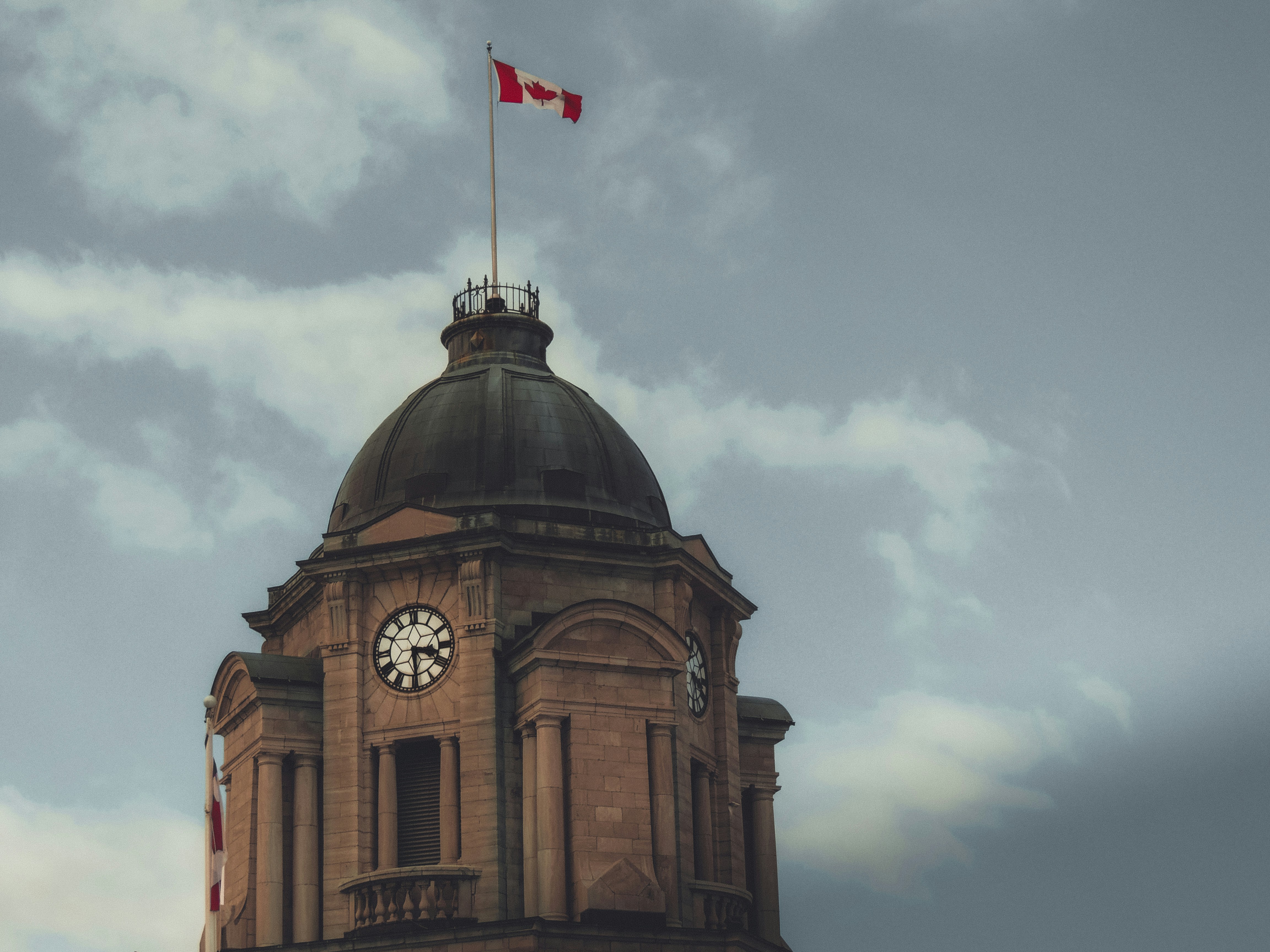 Historic clocktower crowned with a Canadian flag under a moody sky, showcasing architectural detail and national pride.