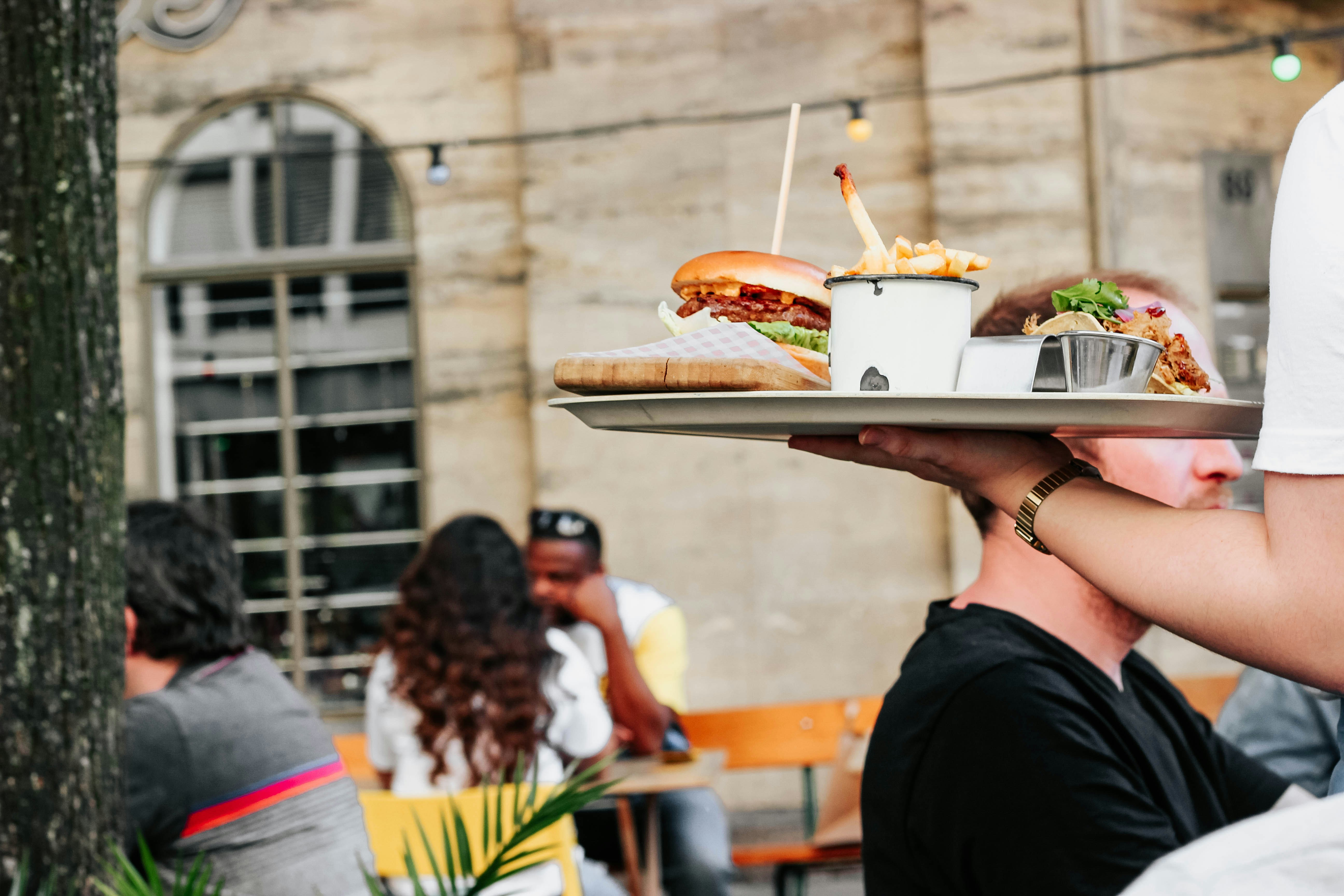 Sunlit Courtyard Tray: Burgers, Fries, and a Busy Café Moment