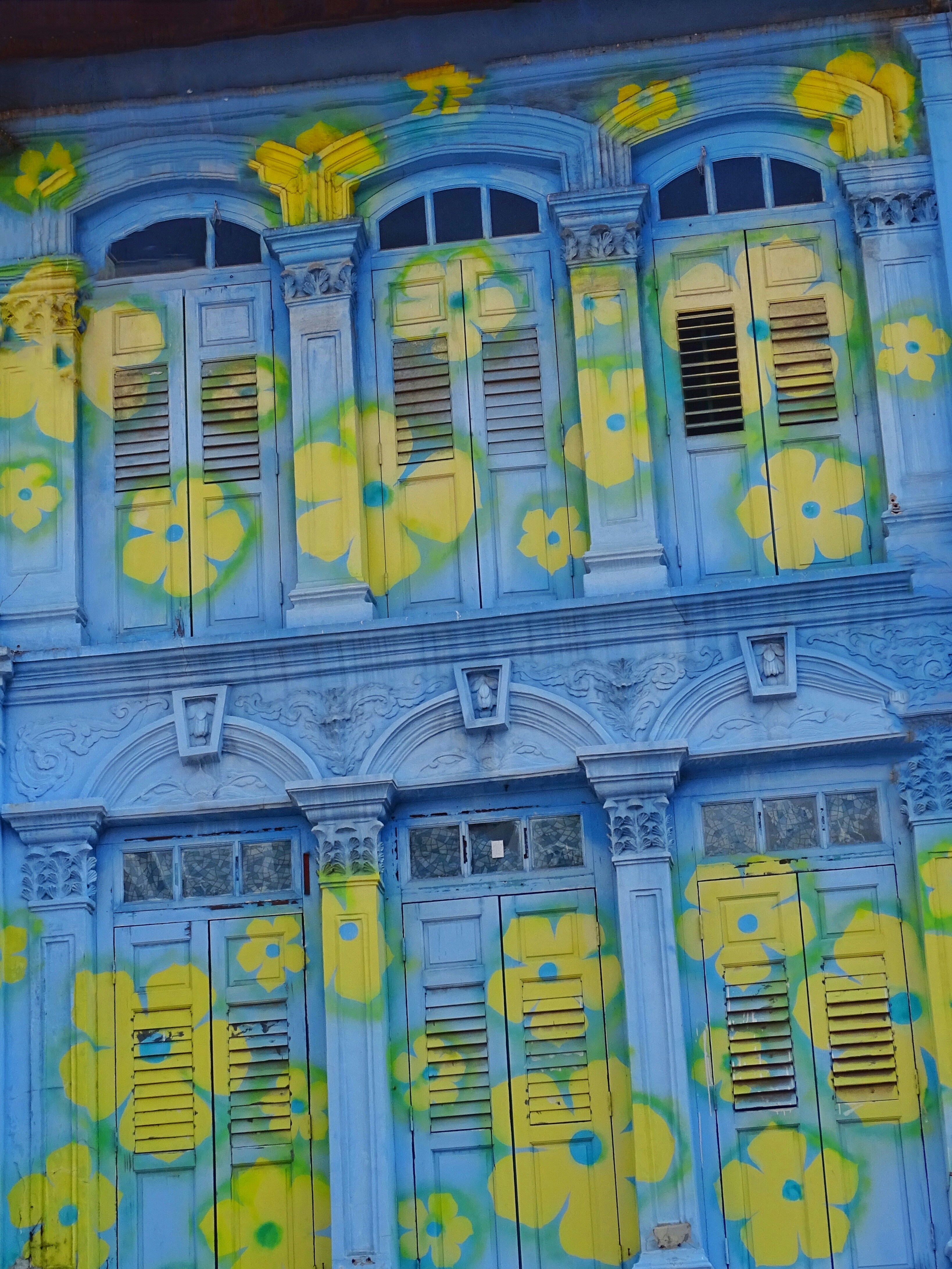 Bright blue wall adorned with yellow flower murals and intricate architectural details. The artwork enhances the building's historical charm.