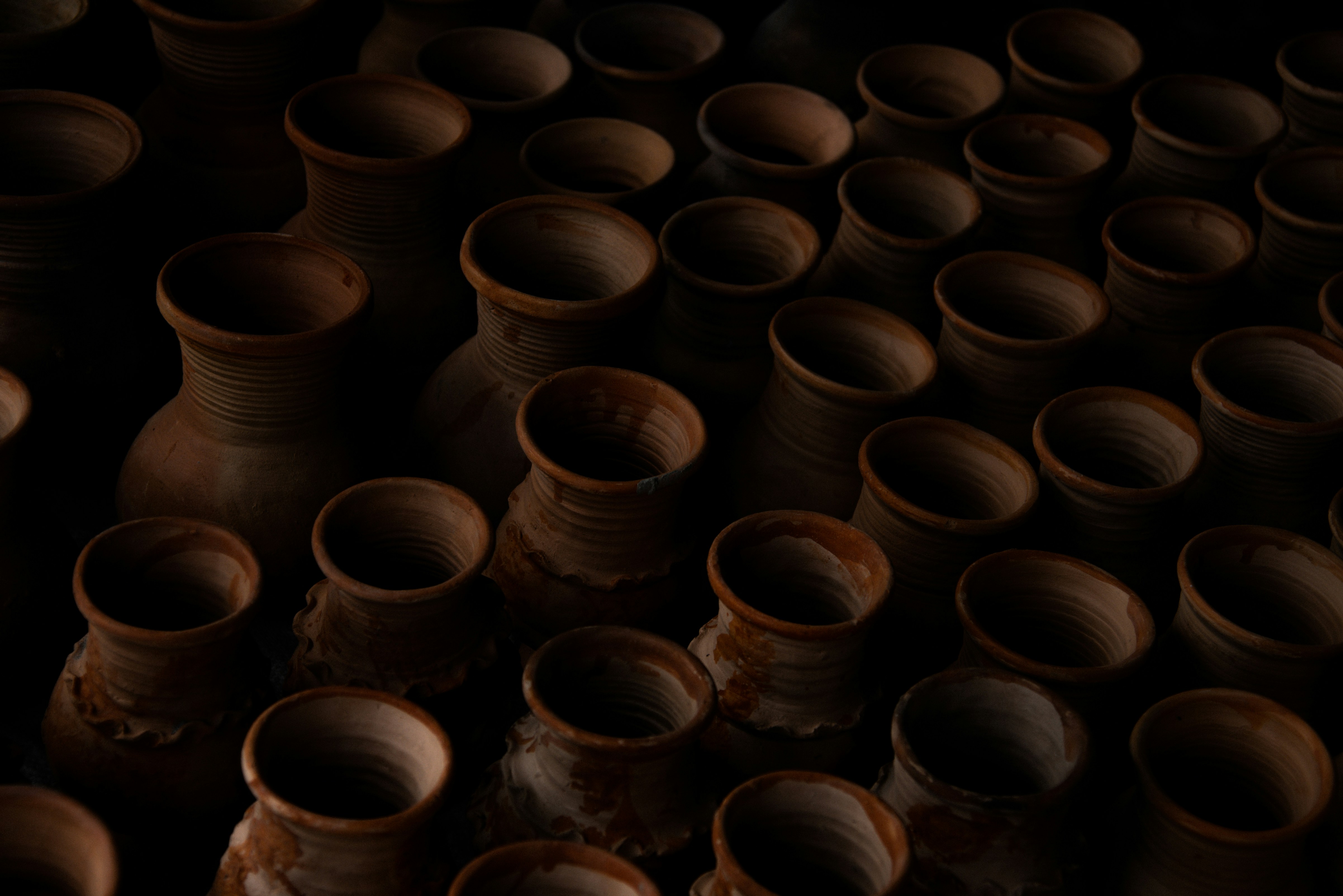 A collection of intricately shaped clay pots arranged closely together, showcasing their earthy tones and textures in a dimly lit environment.