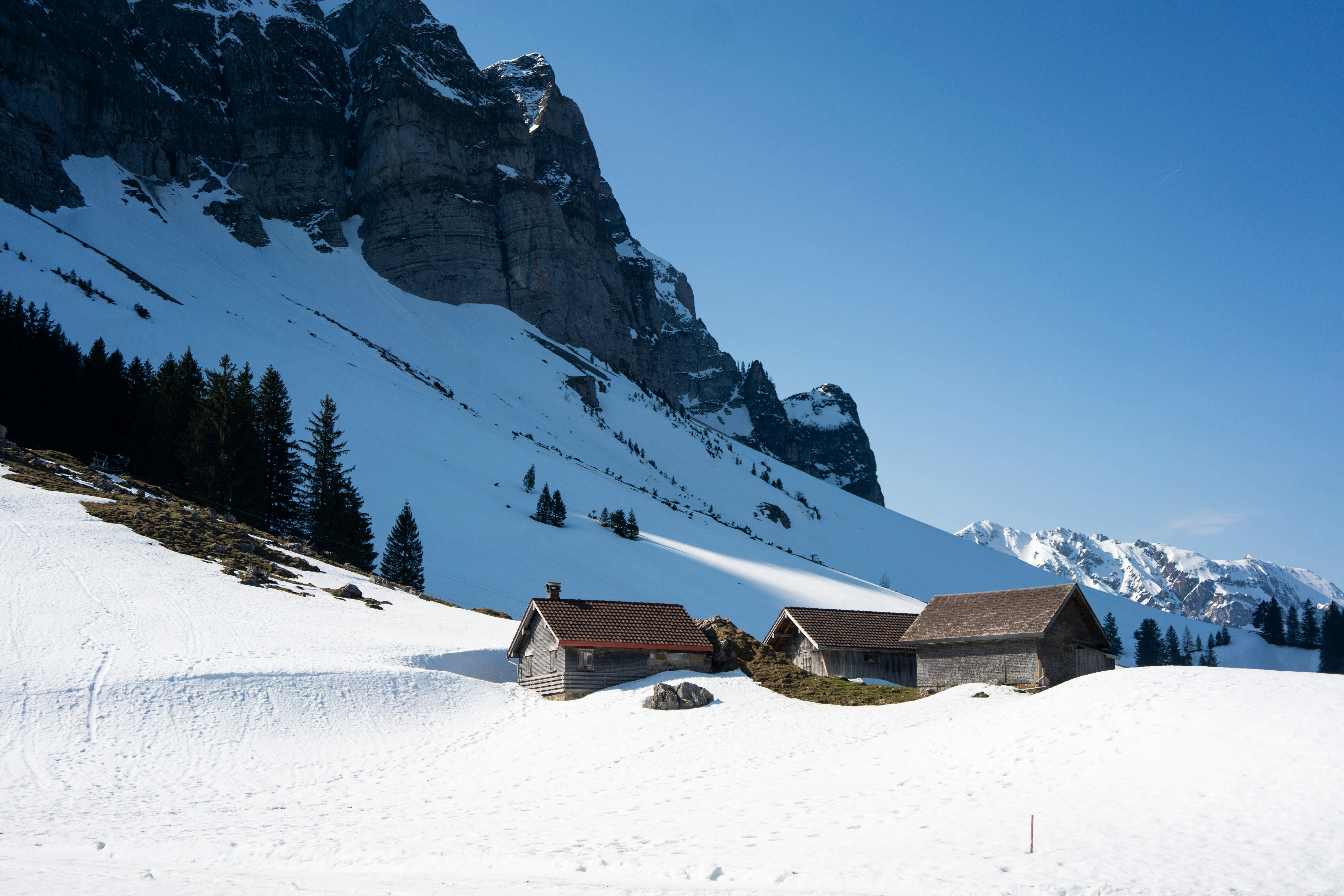 Snow-covered cabins nestled at the base of a towering mountain in Switzerland.