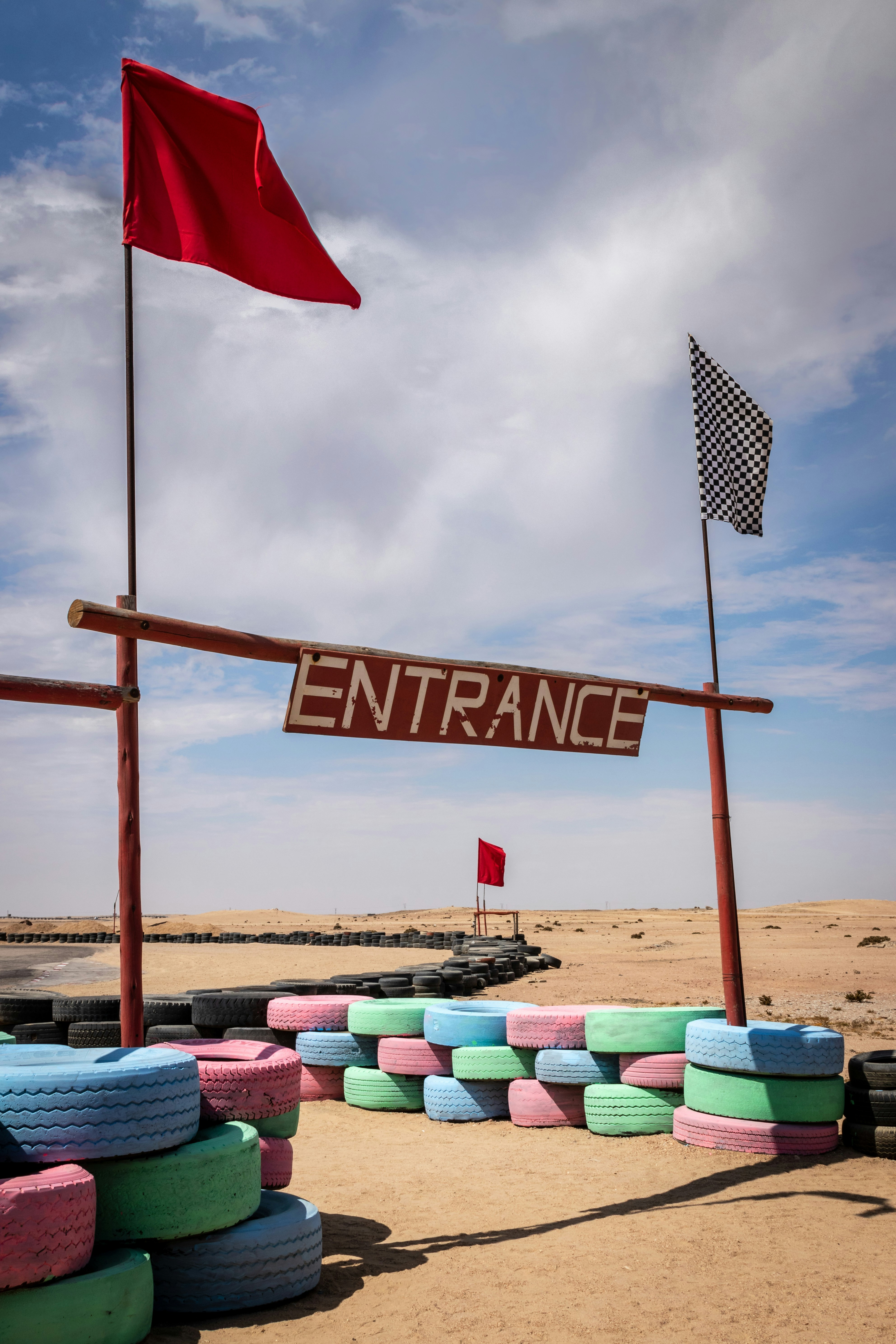 Pastel Tire Barricade: The Desert Raceway Entrance Under Windy Flags