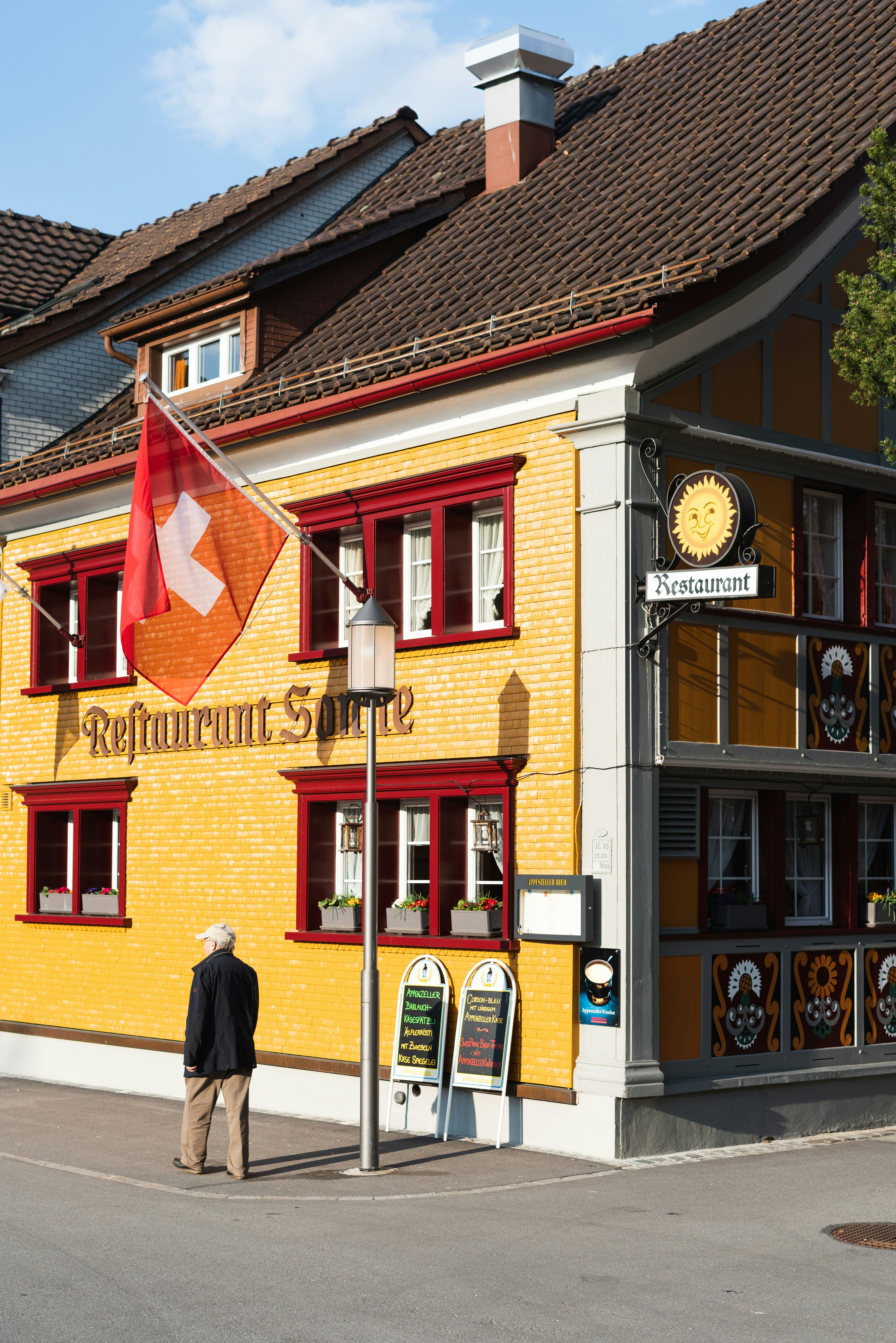 Sunlit Sonne: Yellow-brick Restaurant Facade with Flag and Red Trim