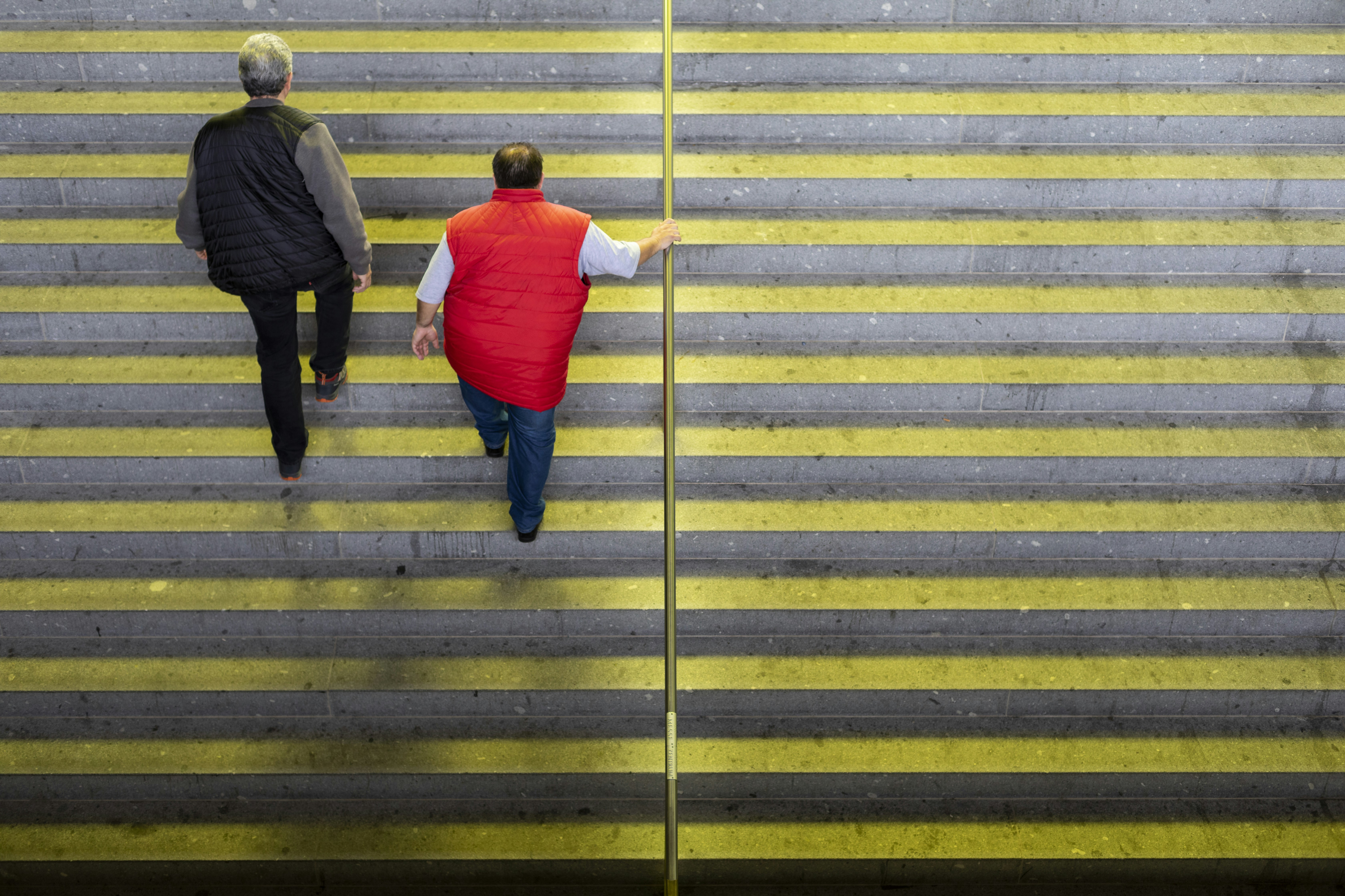 Red Vest on Yellow Rungs: A Top-Down Moment on the Staircase