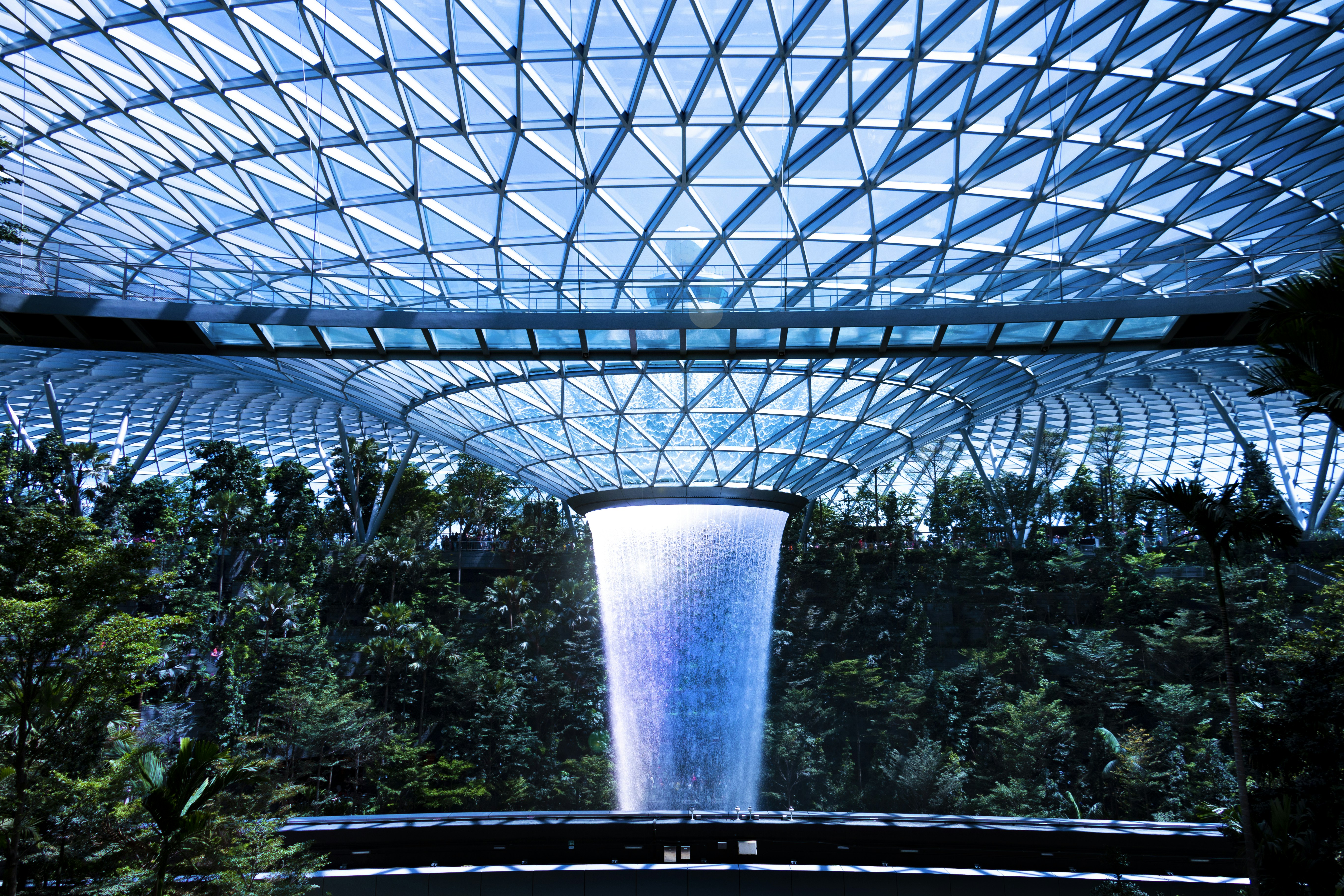 Indoor waterfall cascading from a geometric glass dome surrounded by lush greenery.