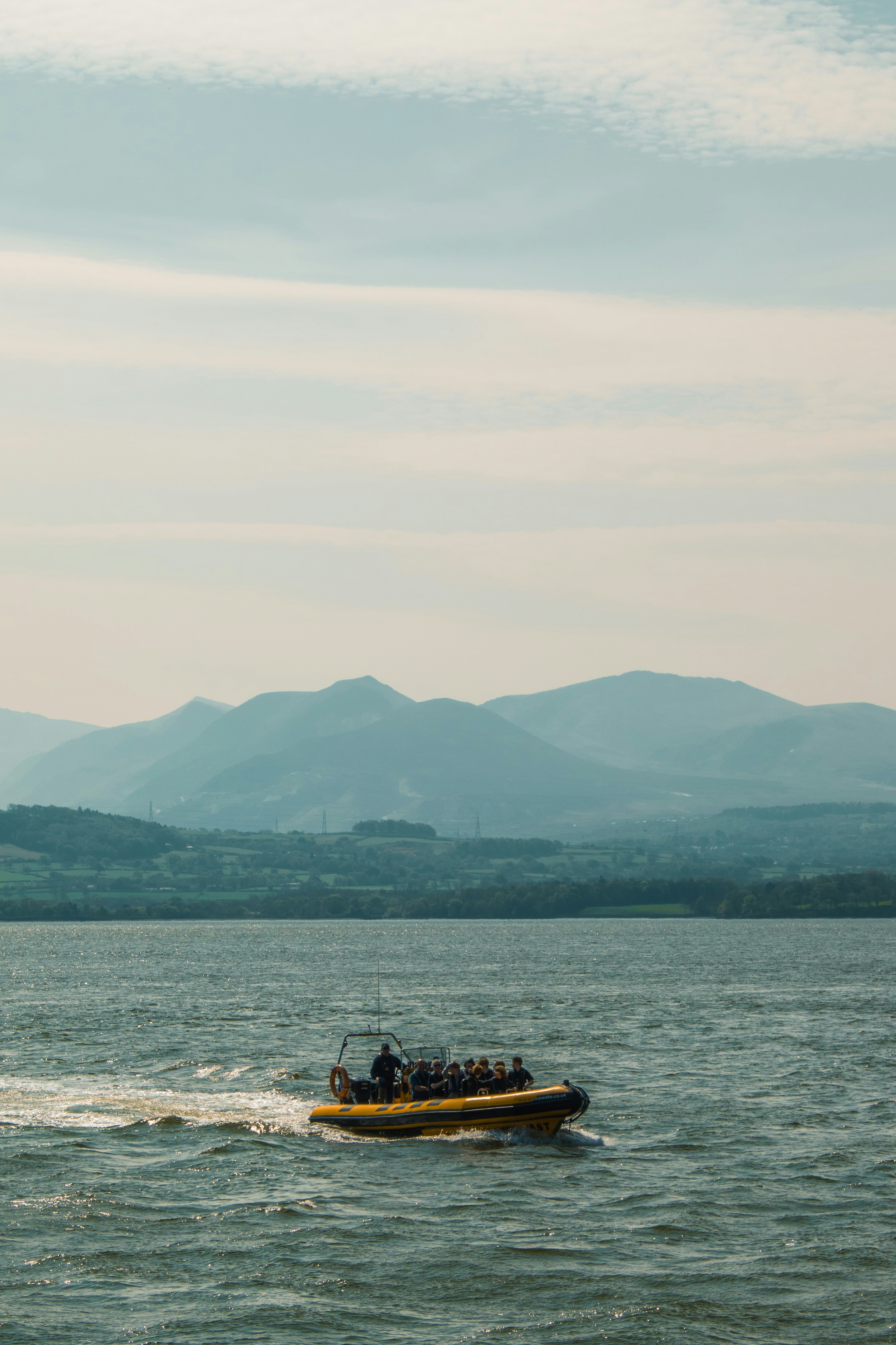 A yellow boat filled with passengers navigates calm waters, with distant mountains providing a scenic backdrop. The serene atmosphere captures the essence of adventure on the open water.