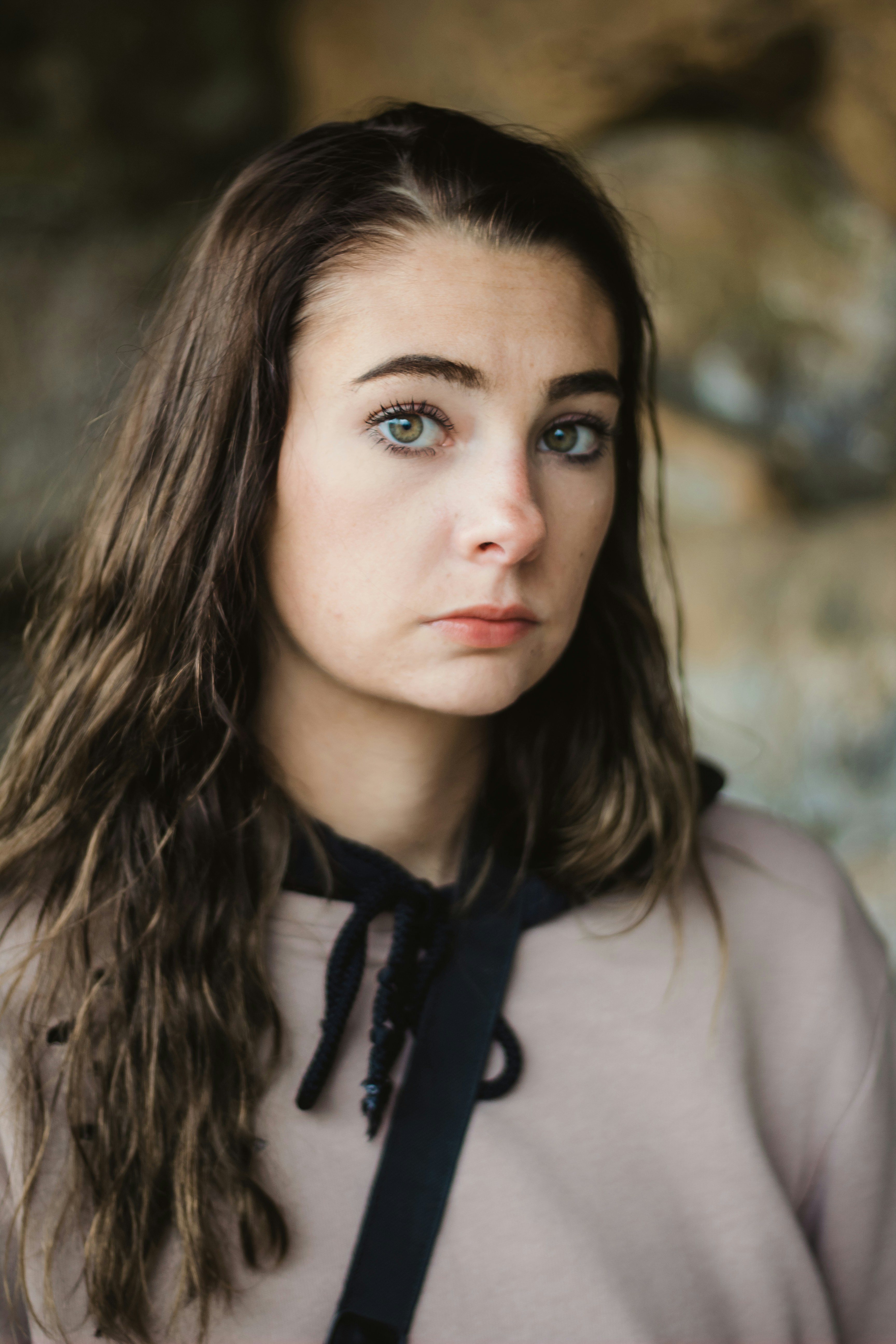 Young woman with long hair gazing thoughtfully, set against a softly blurred natural background.