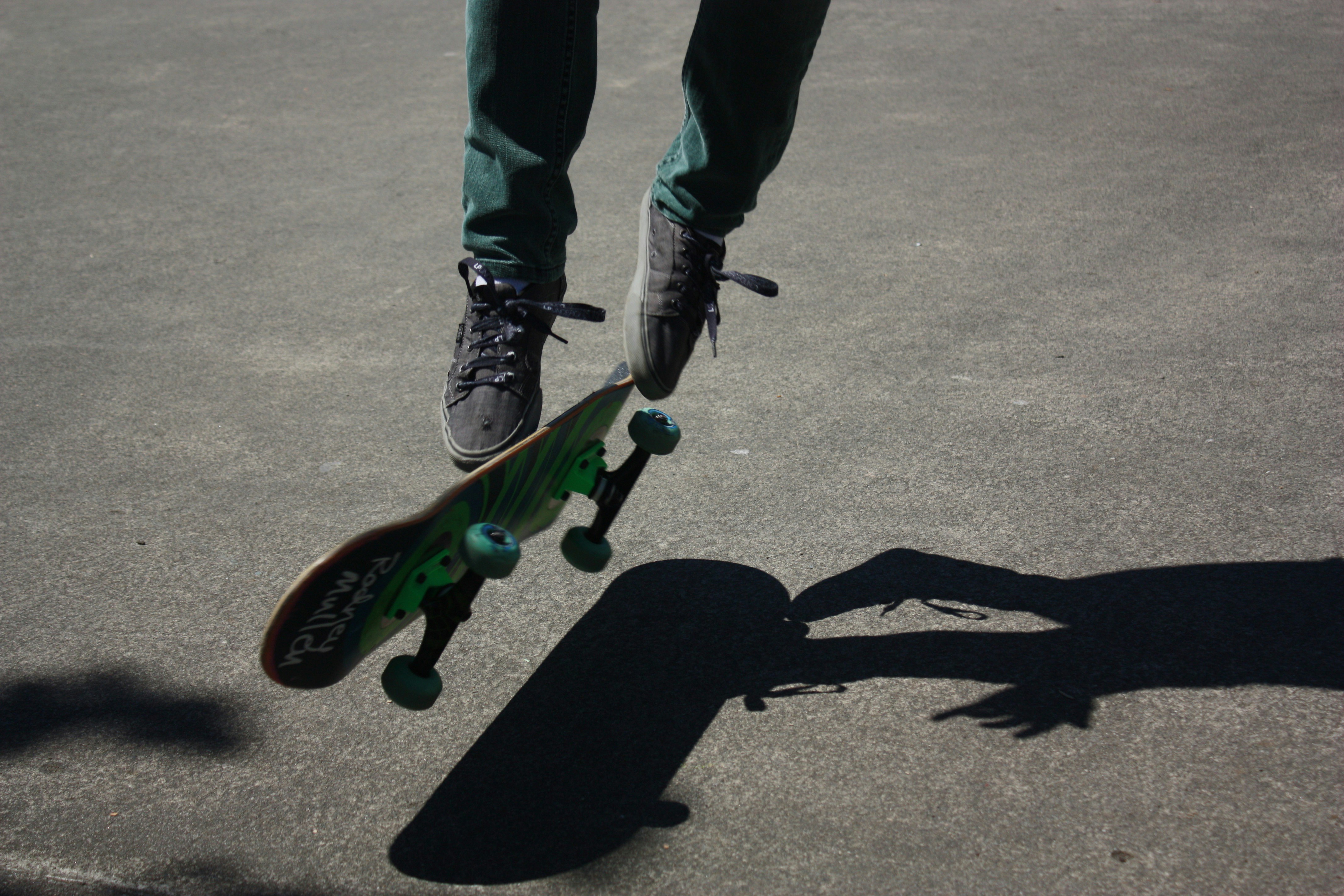 A skateboarder performs an impressive trick, capturing the moment of lift as the board hovers mid-air above the ground. The shadow adds depth to the dynamic scene.