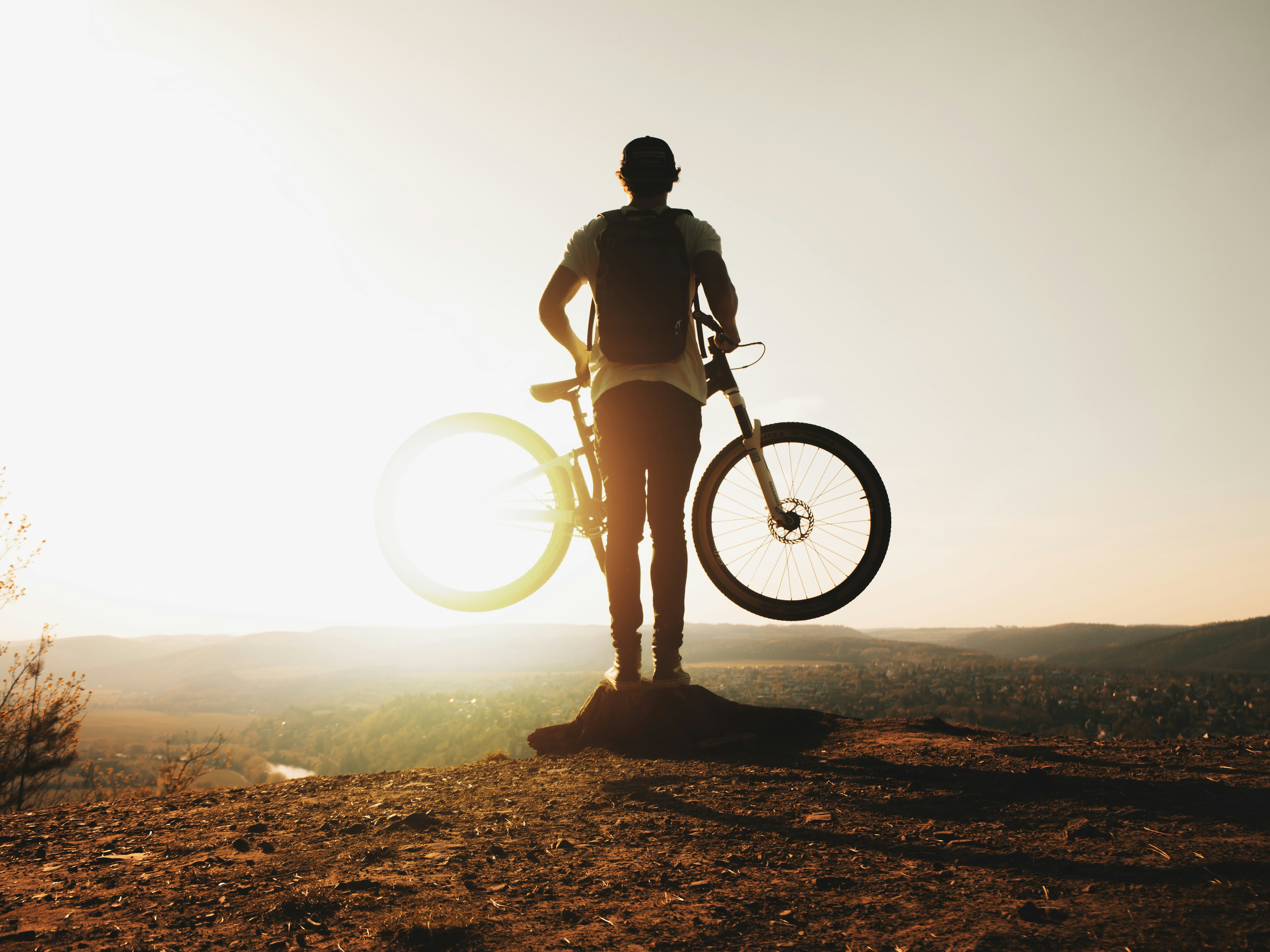 Silhouette of a cyclist holding a mountain bike against a sunset backdrop, symbolizing adventure and exploration.