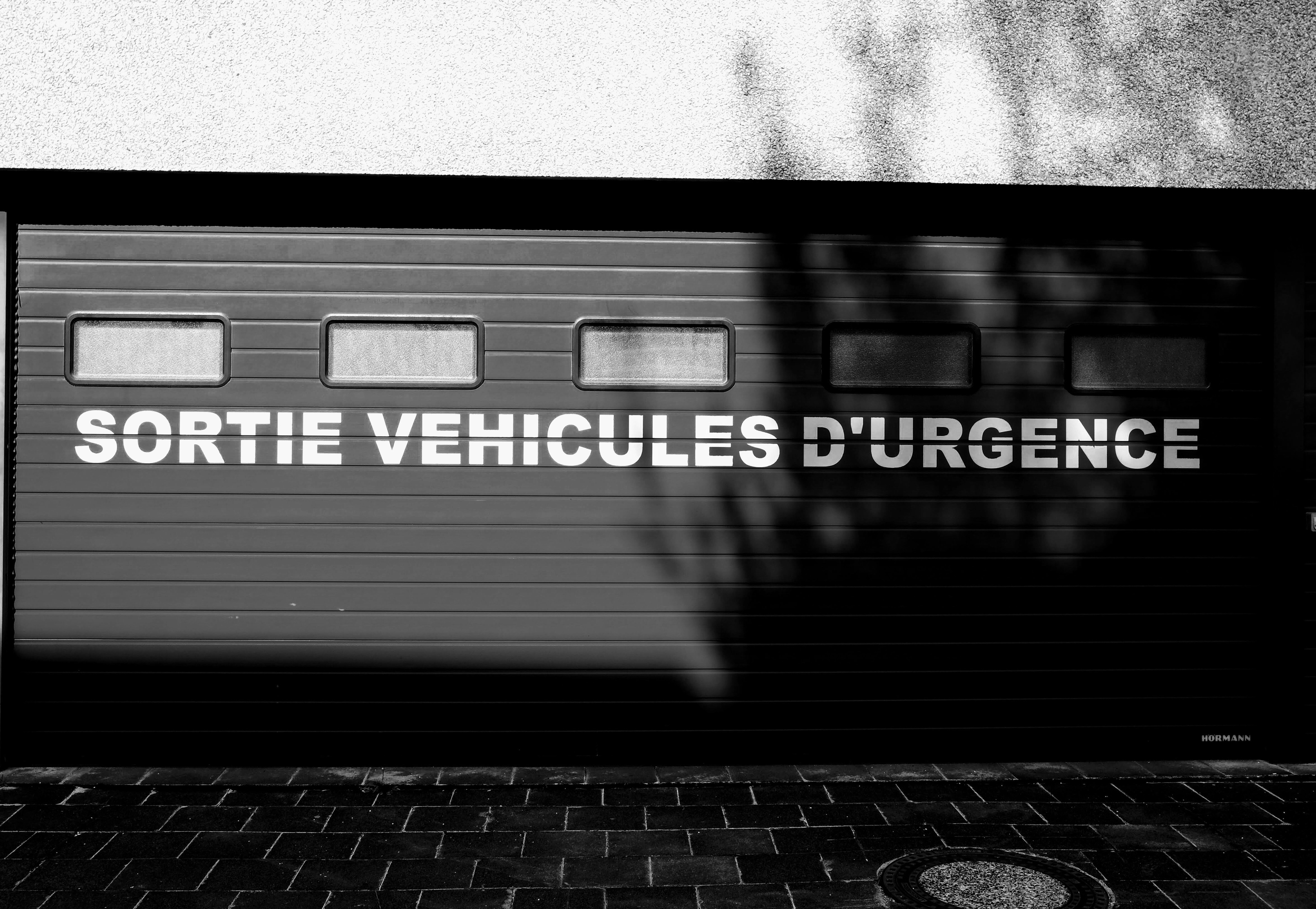 Urgence Gate in Monochrome: Bold French Sign Under a Shadowed Facade