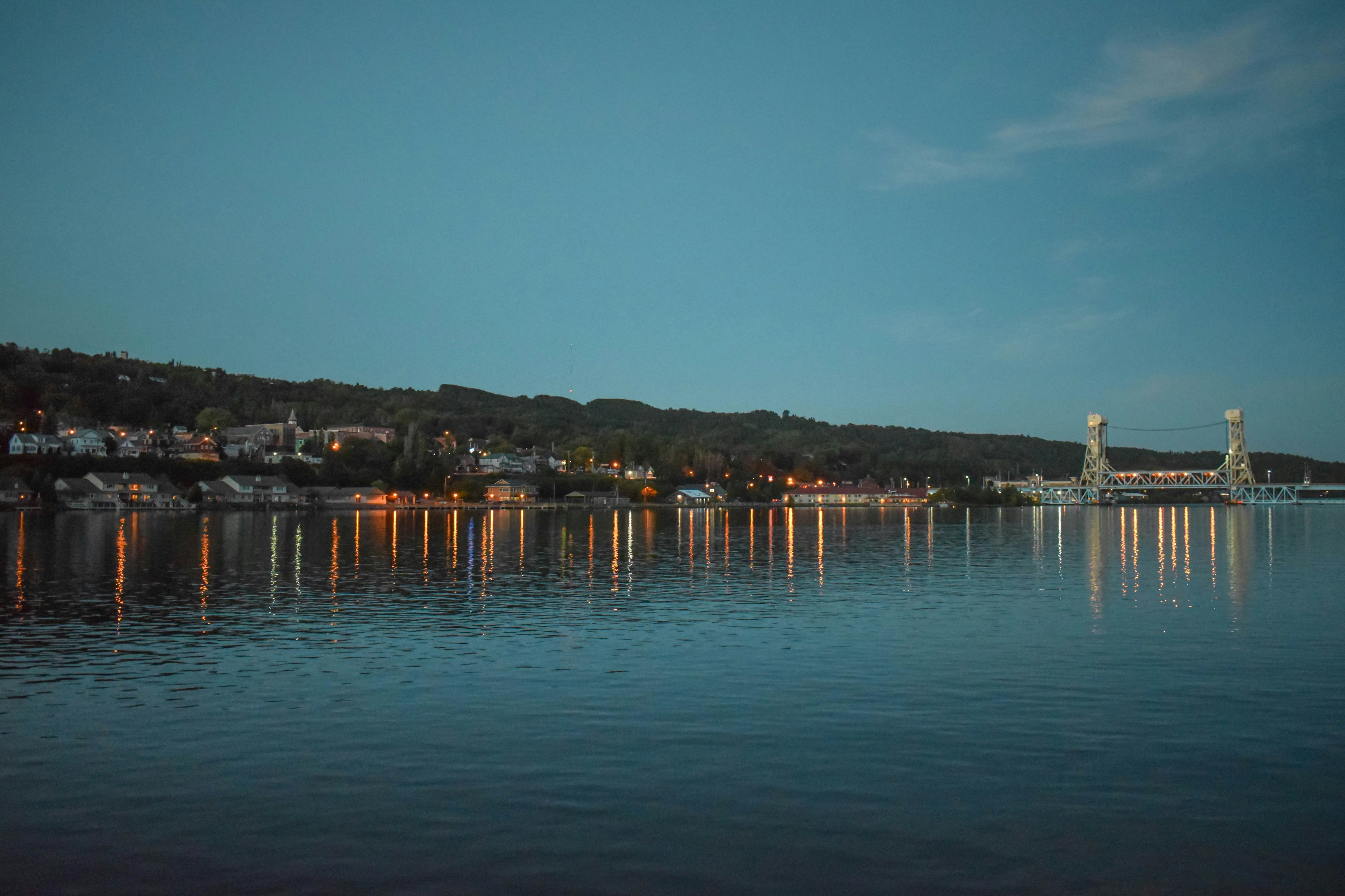 Coastal town with illuminated buildings reflecting on calm water at dusk.