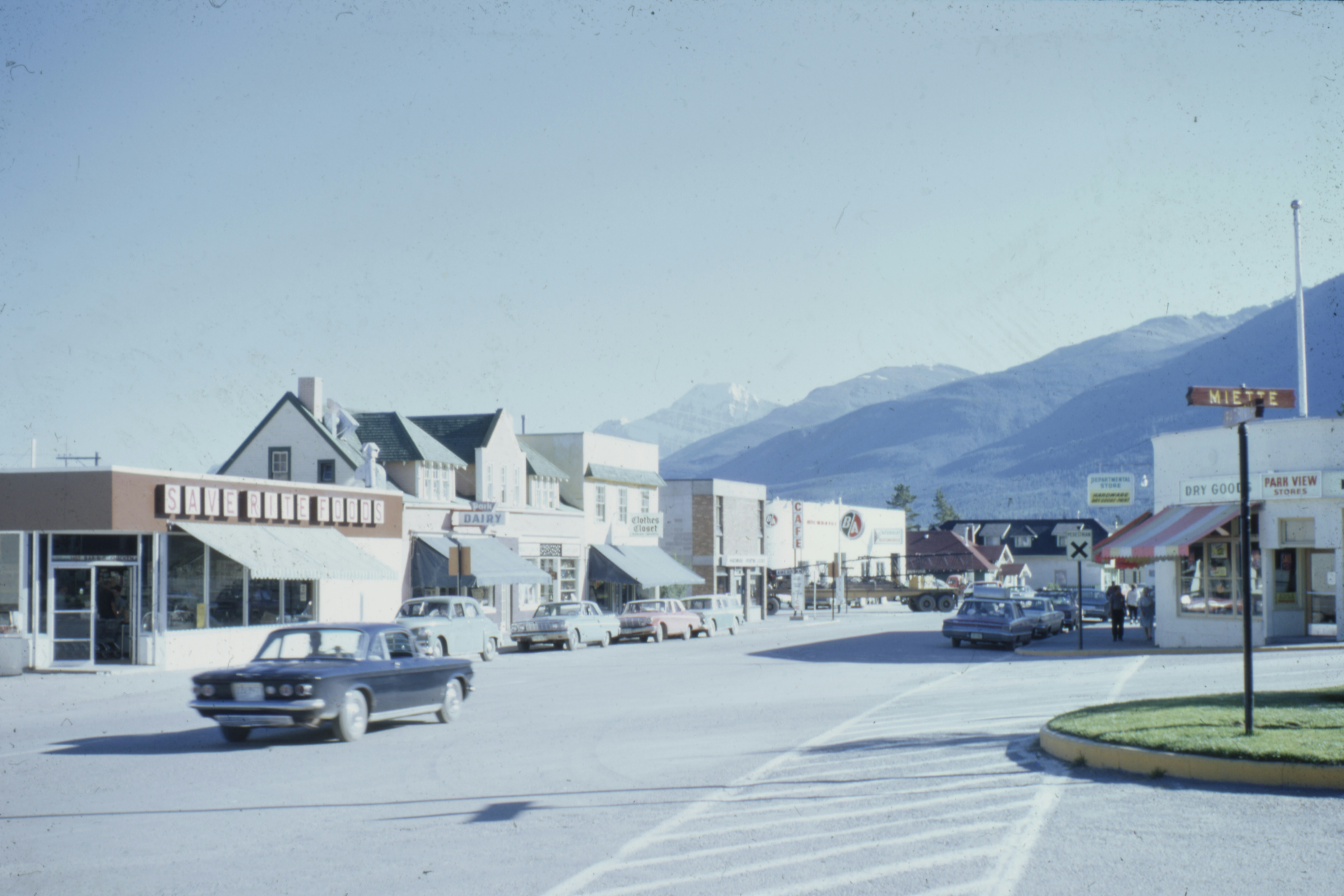 Retro cars parked along a quiet street with mountain views under a clear blue sky.