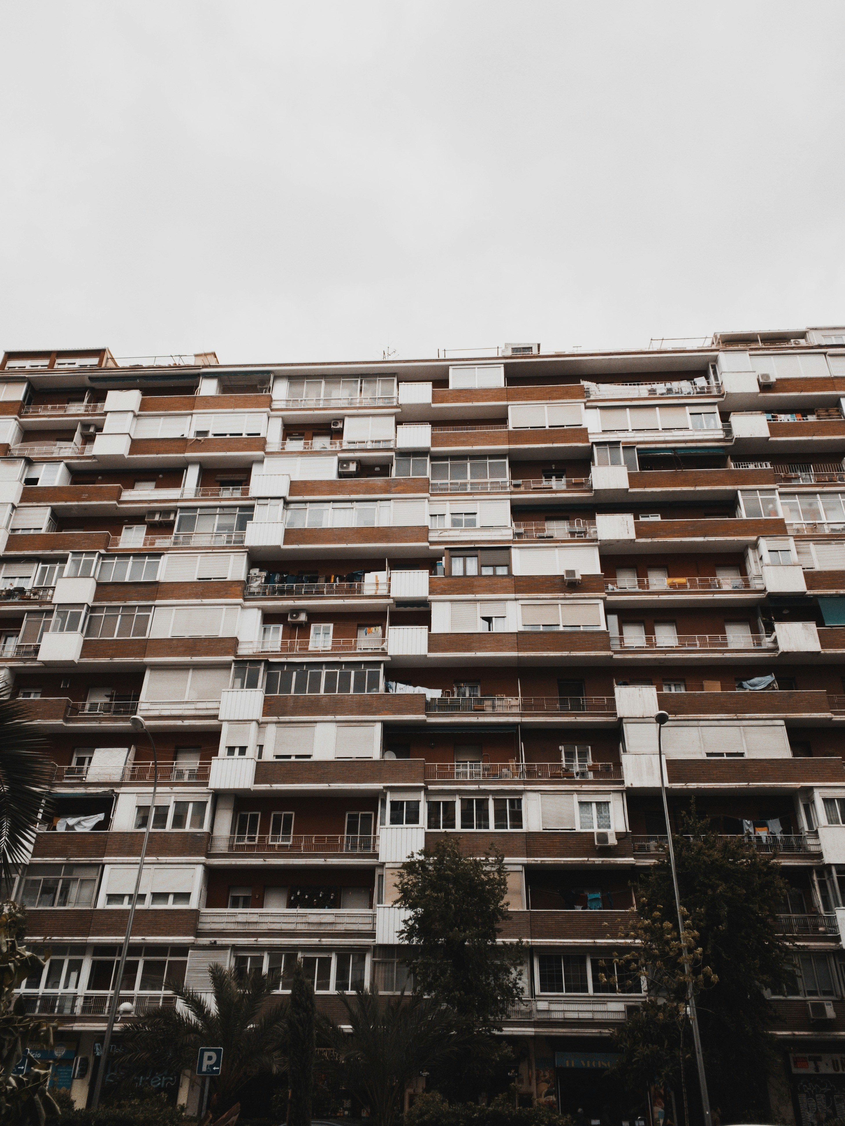 Architectural facade of a residential building showcasing a rhythmic pattern of windows and balconies. The cloudy sky adds a muted backdrop to the structured lines.