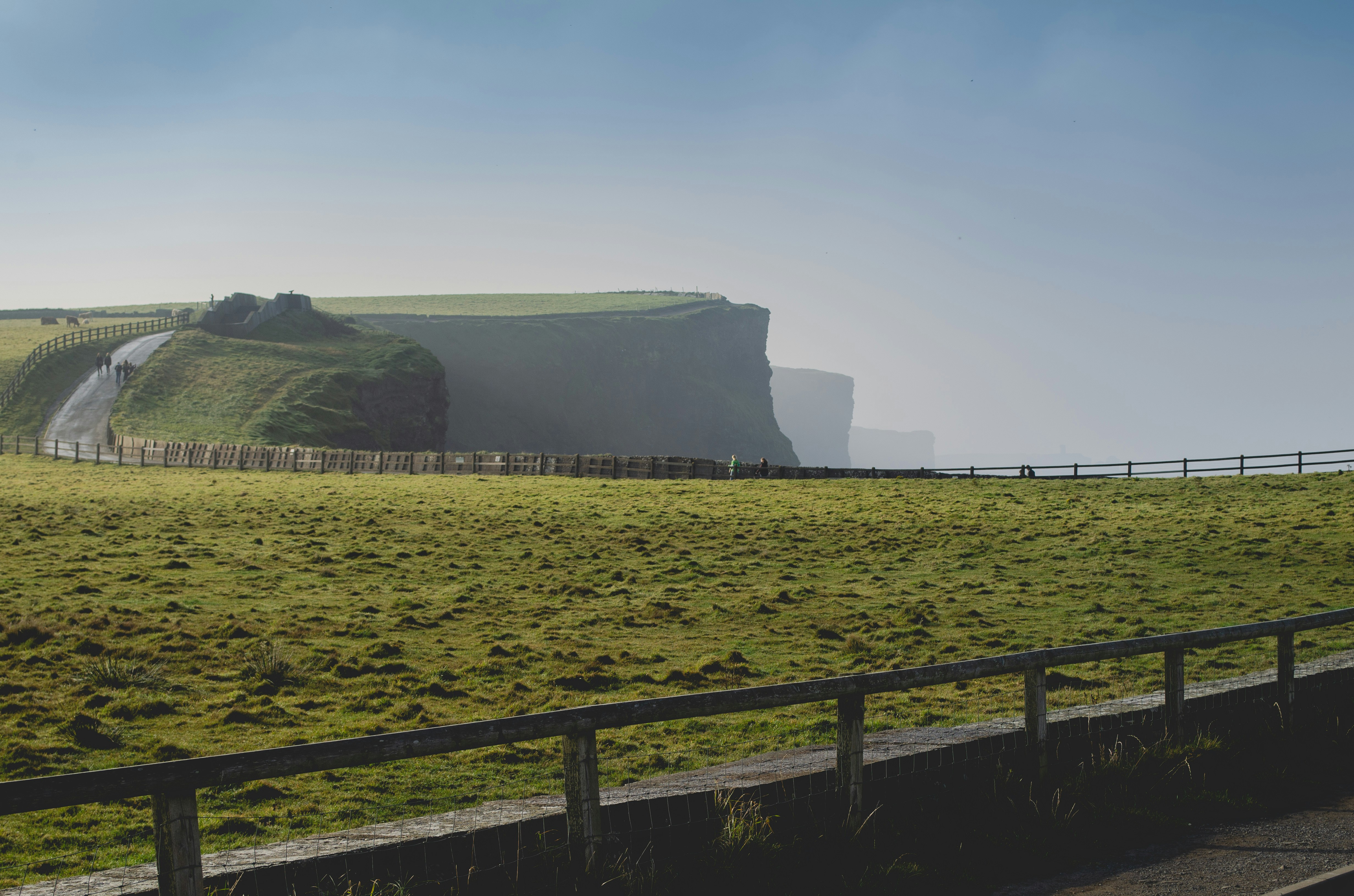 Rolling green hills meet dramatic cliffs under a misty sky, inviting tranquility and exploration. The scene captures the essence of coastal beauty.