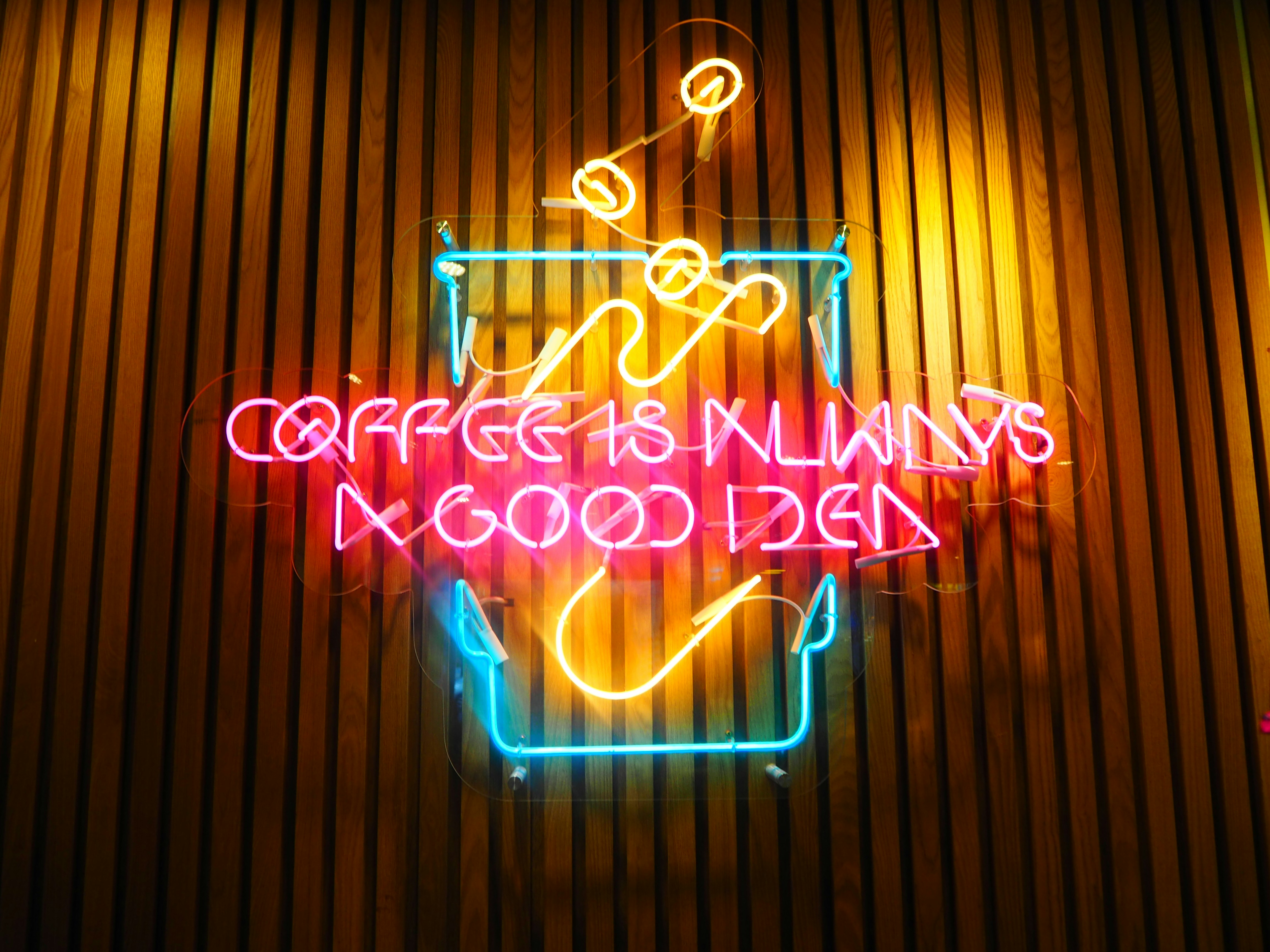 Vibrant neon sign featuring the phrase 'Coffee is always a good idea' against a wooden backdrop.