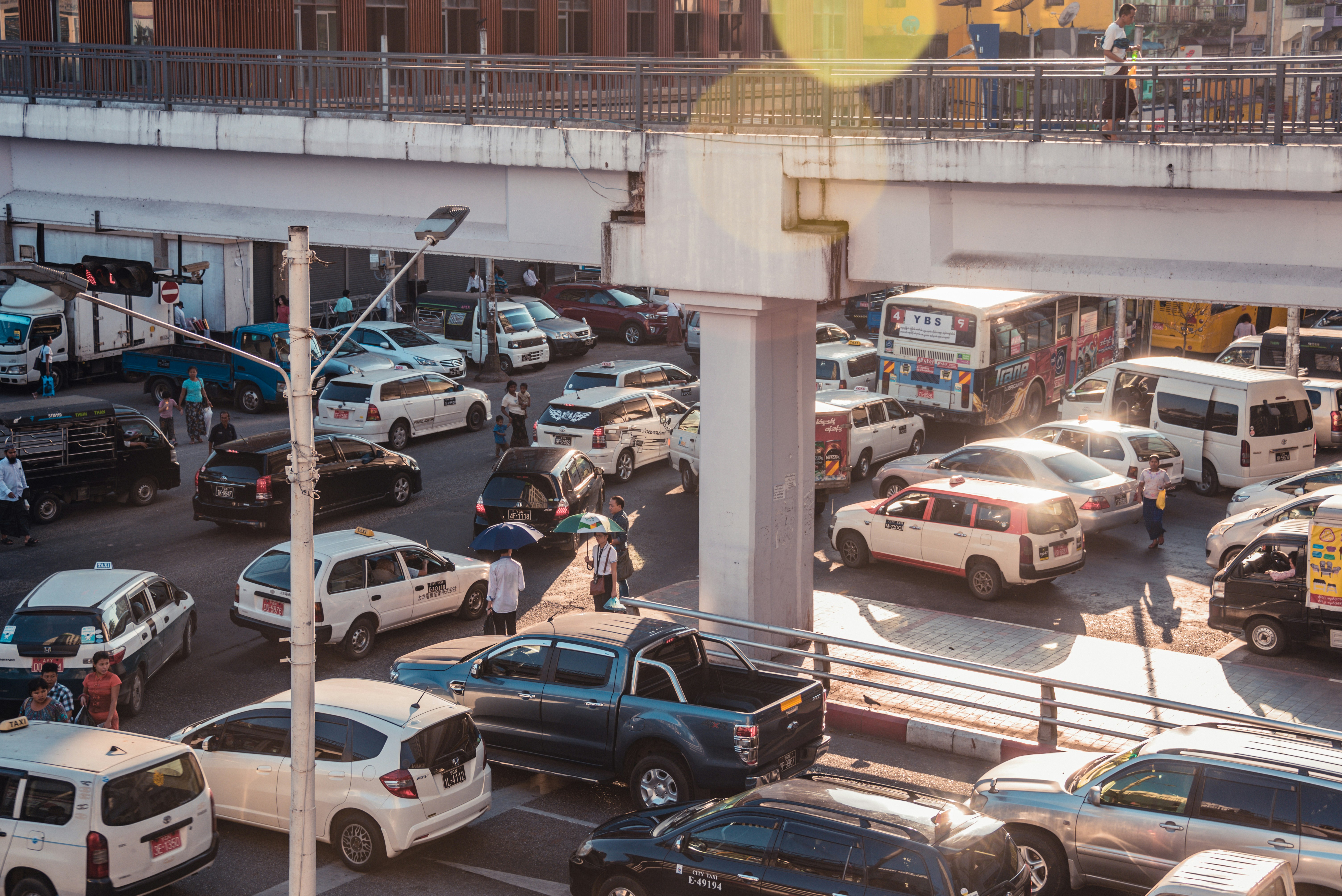 Traffic congestion beneath an overpass in Yangon during dusk, with vehicles and pedestrians navigating the bustling intersection.