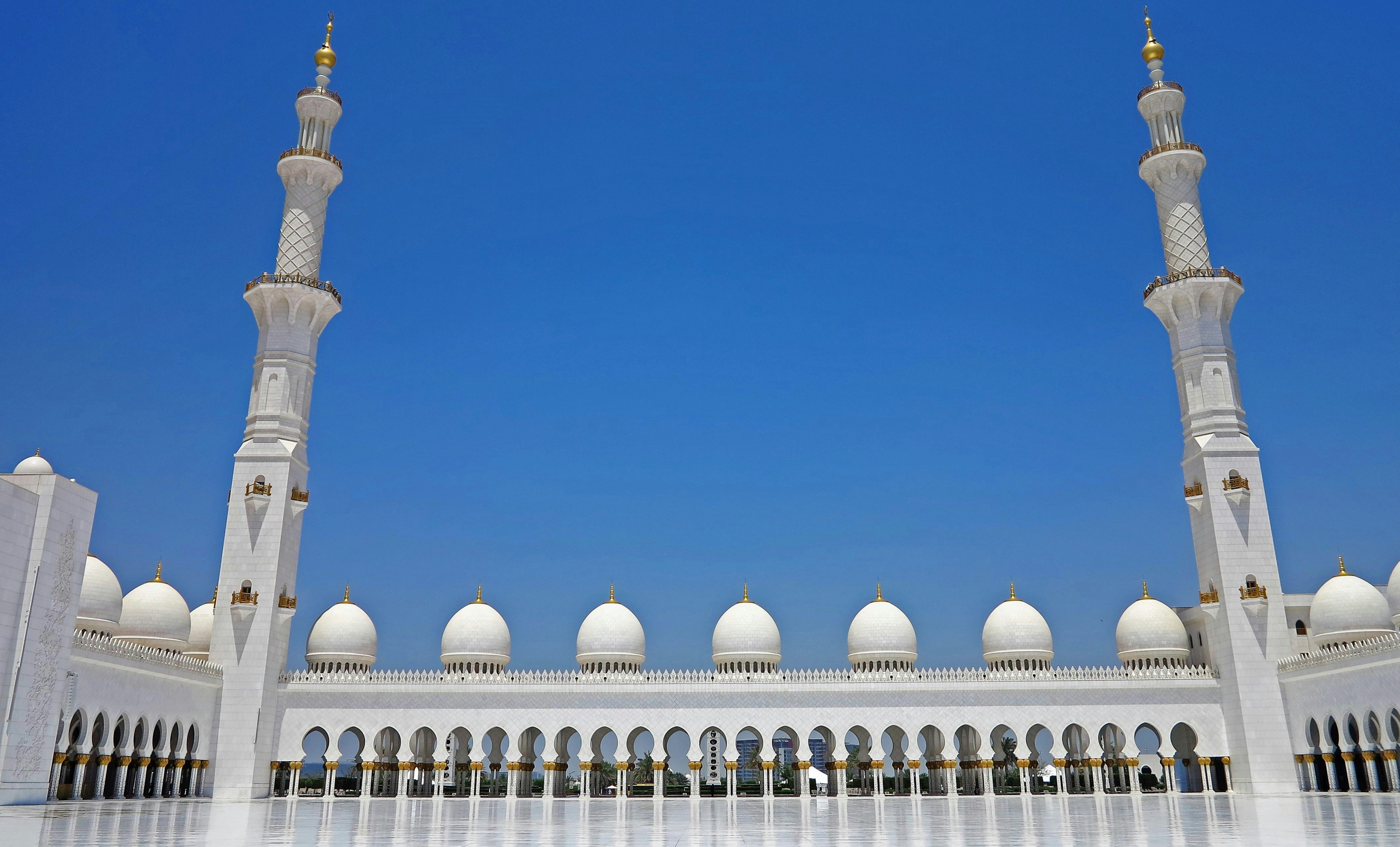 Majestic mosque showcasing intricate white architecture against a clear blue sky, with towering minarets and domes reflecting Islamic artistry.