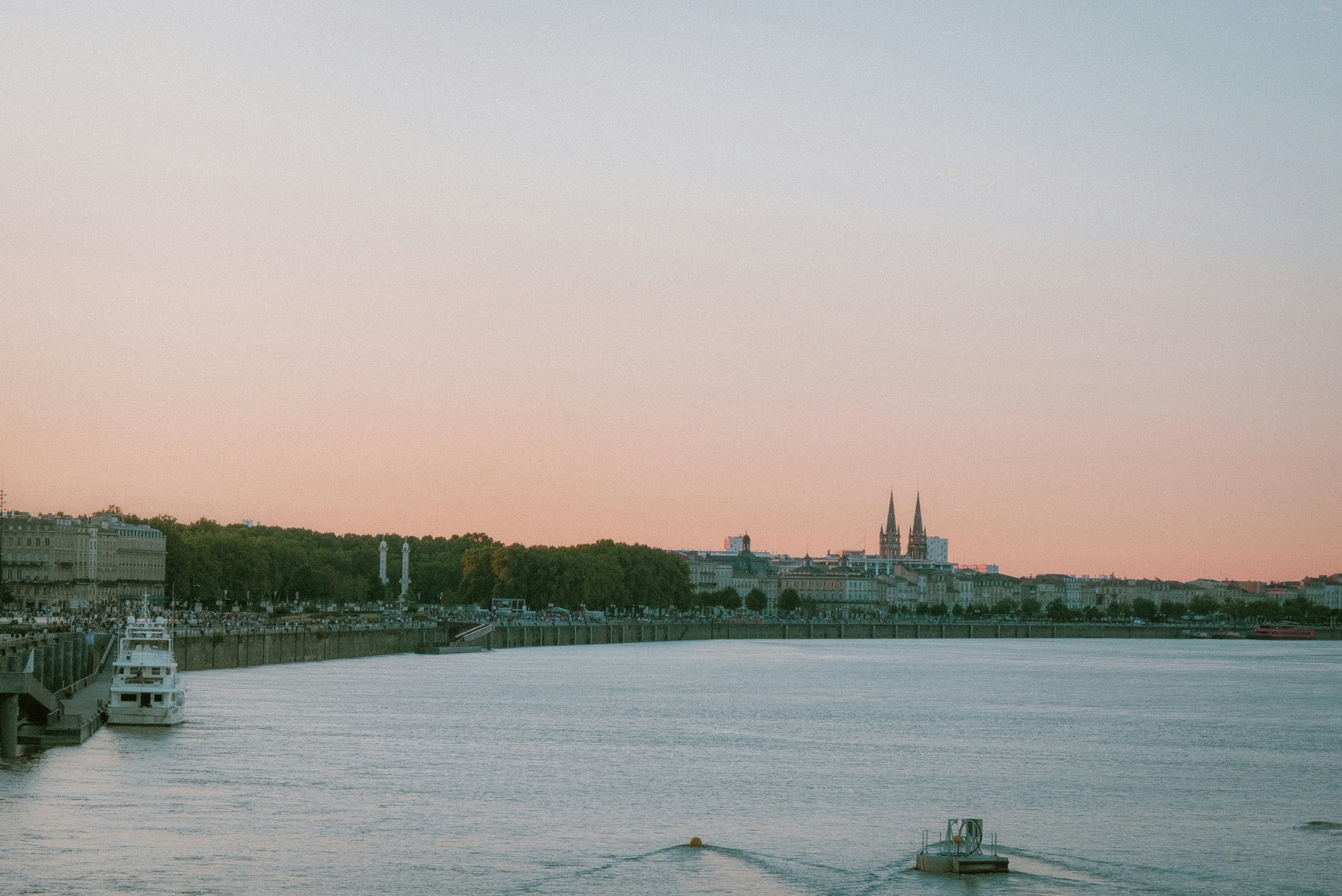 White boat gliding along a wide river at sunset with distant city skyline.