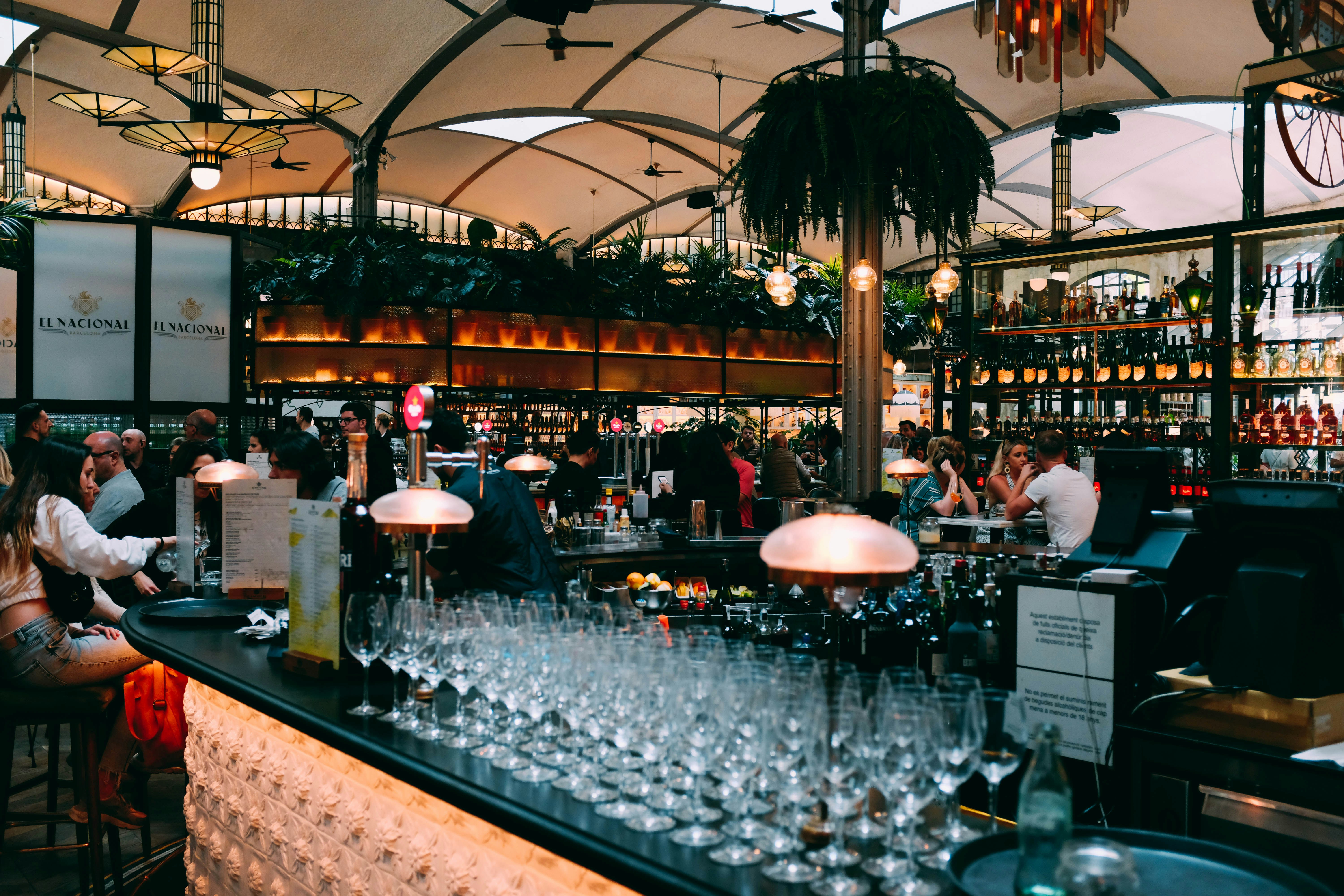Elegant bar scene filled with patrons enjoying drinks in a lively atmosphere, surrounded by shelves of spirits and ambient lighting.