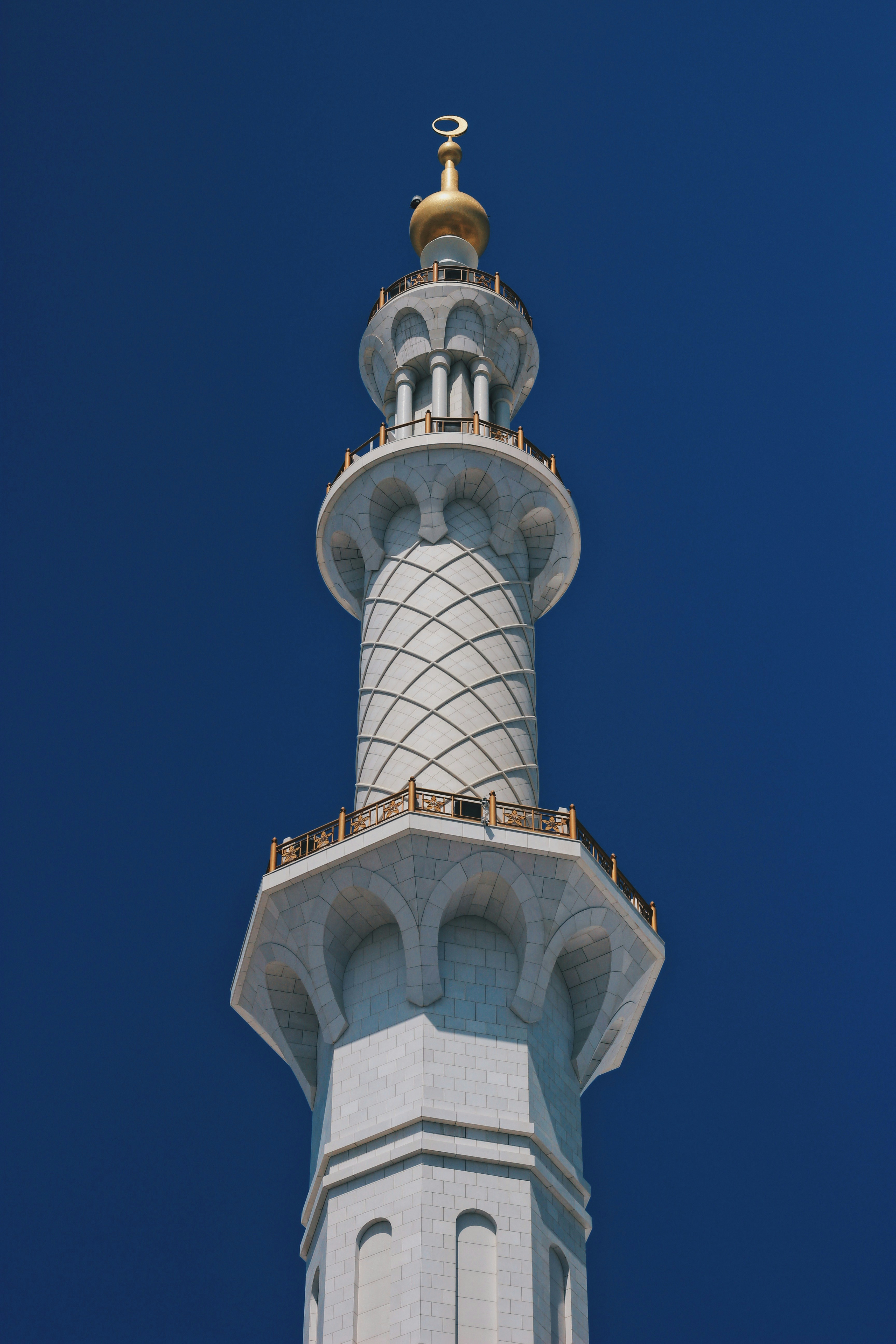 Elegant minaret adorned with intricate designs and a golden finial against a clear blue sky.