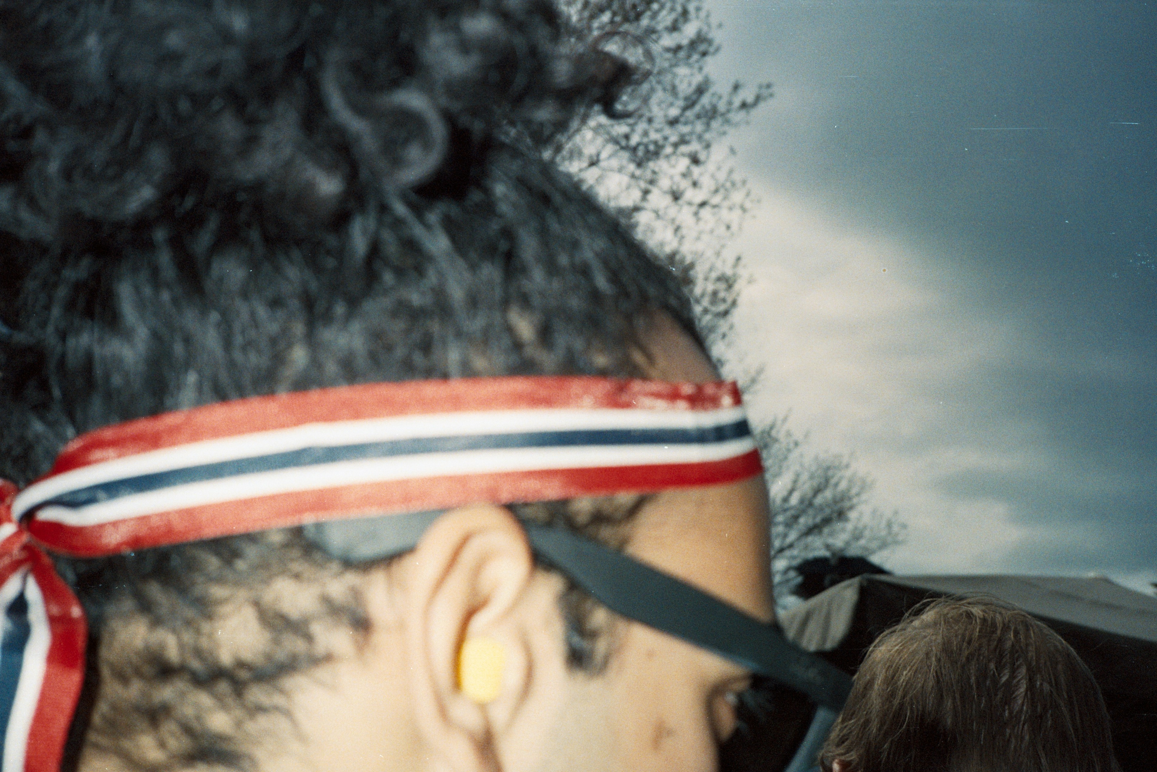 Close-up of a person wearing a red, white, and blue headband and an ear guard. Outdoor light with a softly blurred background.