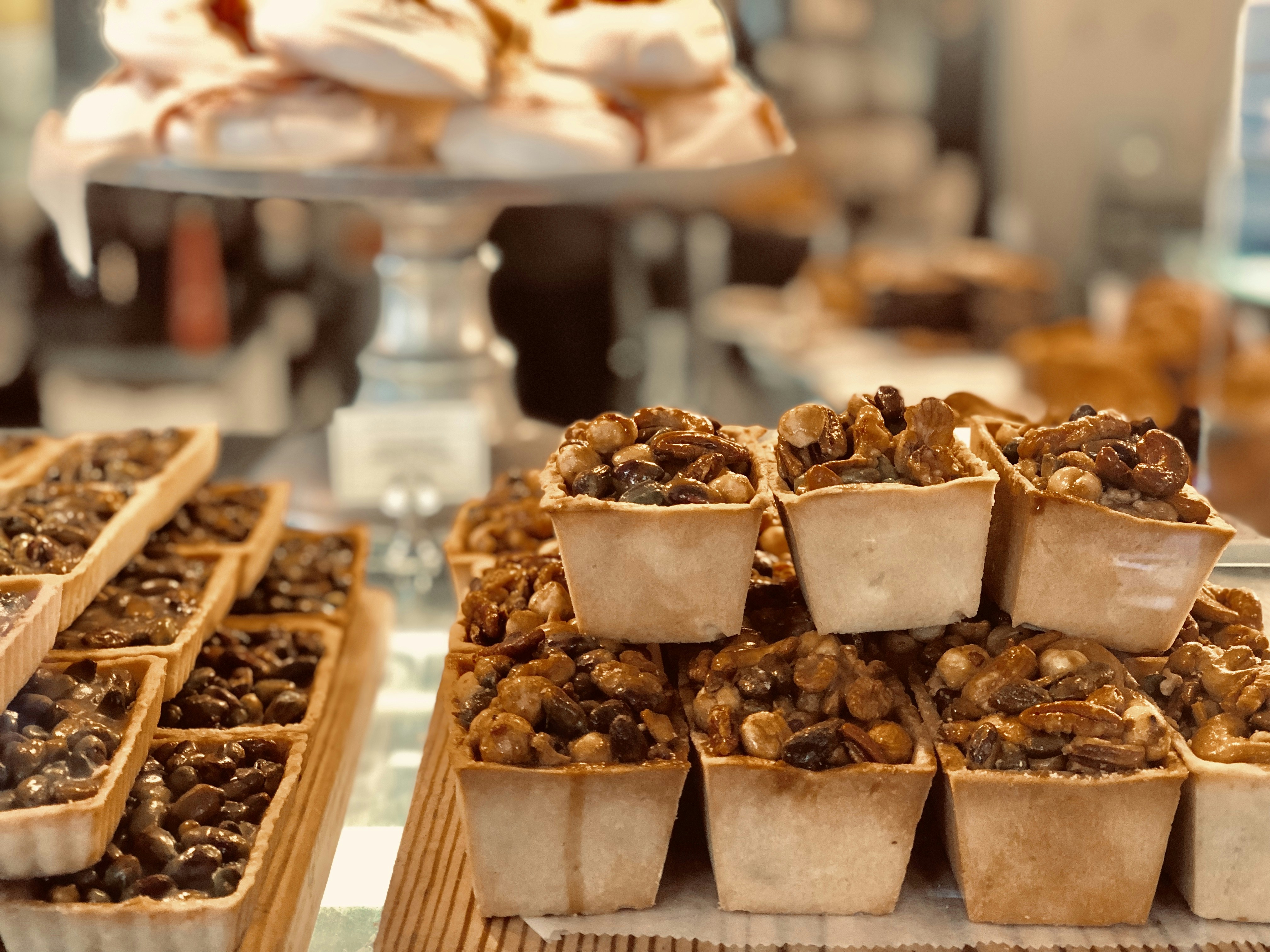A display of assorted pastries, featuring nut-filled tartlets in the foreground and elegant meringues in the background. The arrangement highlights the artistry of dessert presentation.