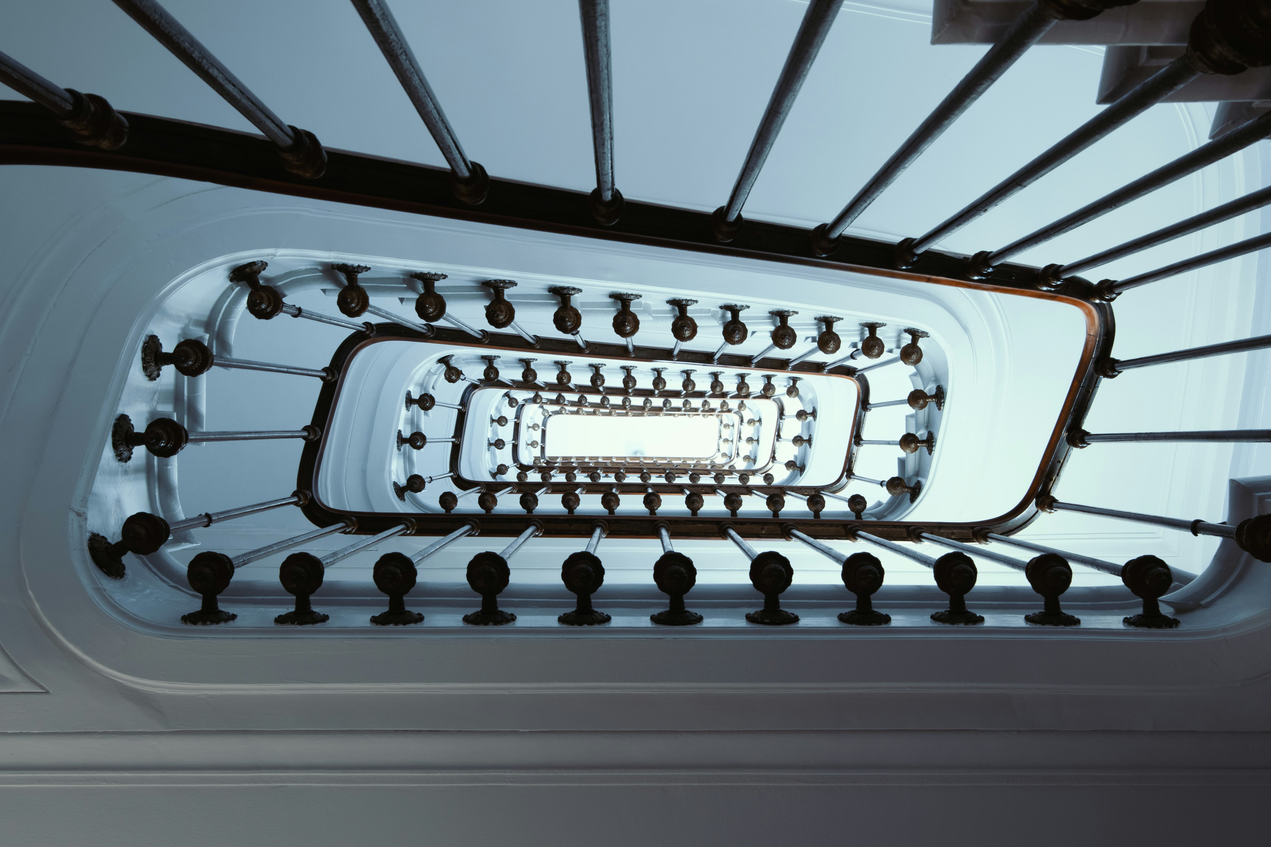 Elegant spiral staircase viewed from above, showcasing intricate railings and a soft gradient of light.