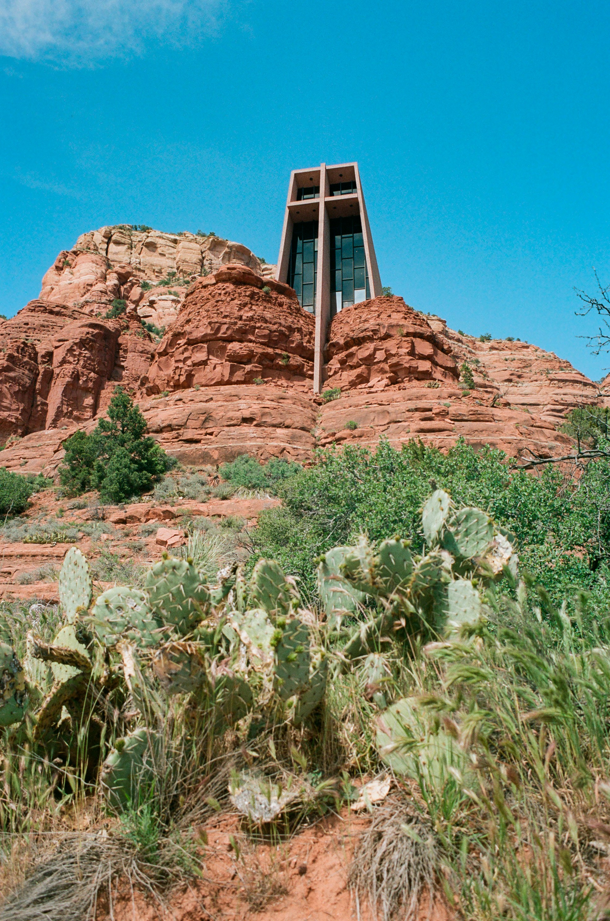 Modern architectural structure rising dramatically from red rock formations, surrounded by desert vegetation and blue sky.
