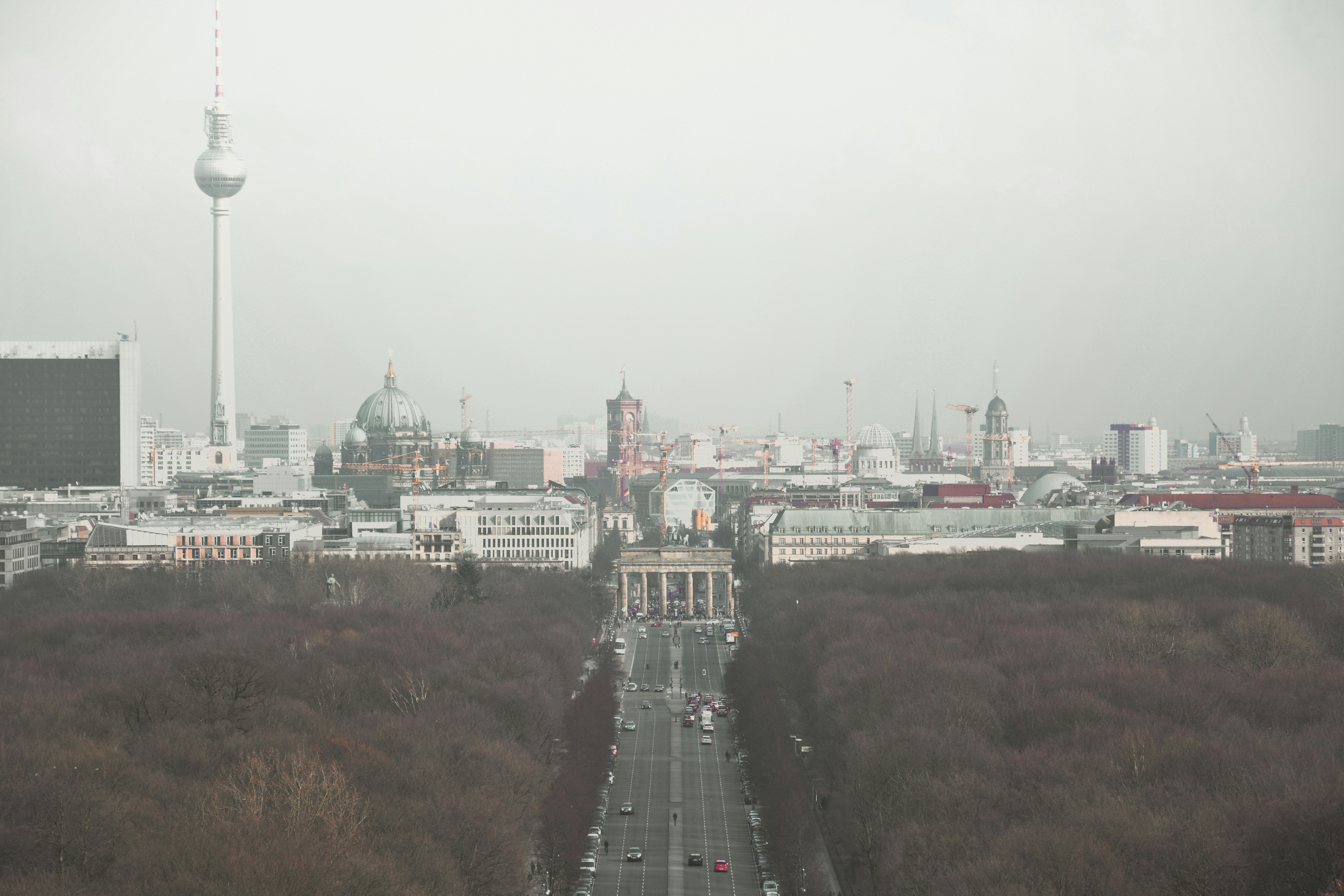 Aerial view of Berlin showcasing the Brandenburg Gate framed by bare trees, with the TV Tower and historic buildings in the background. 