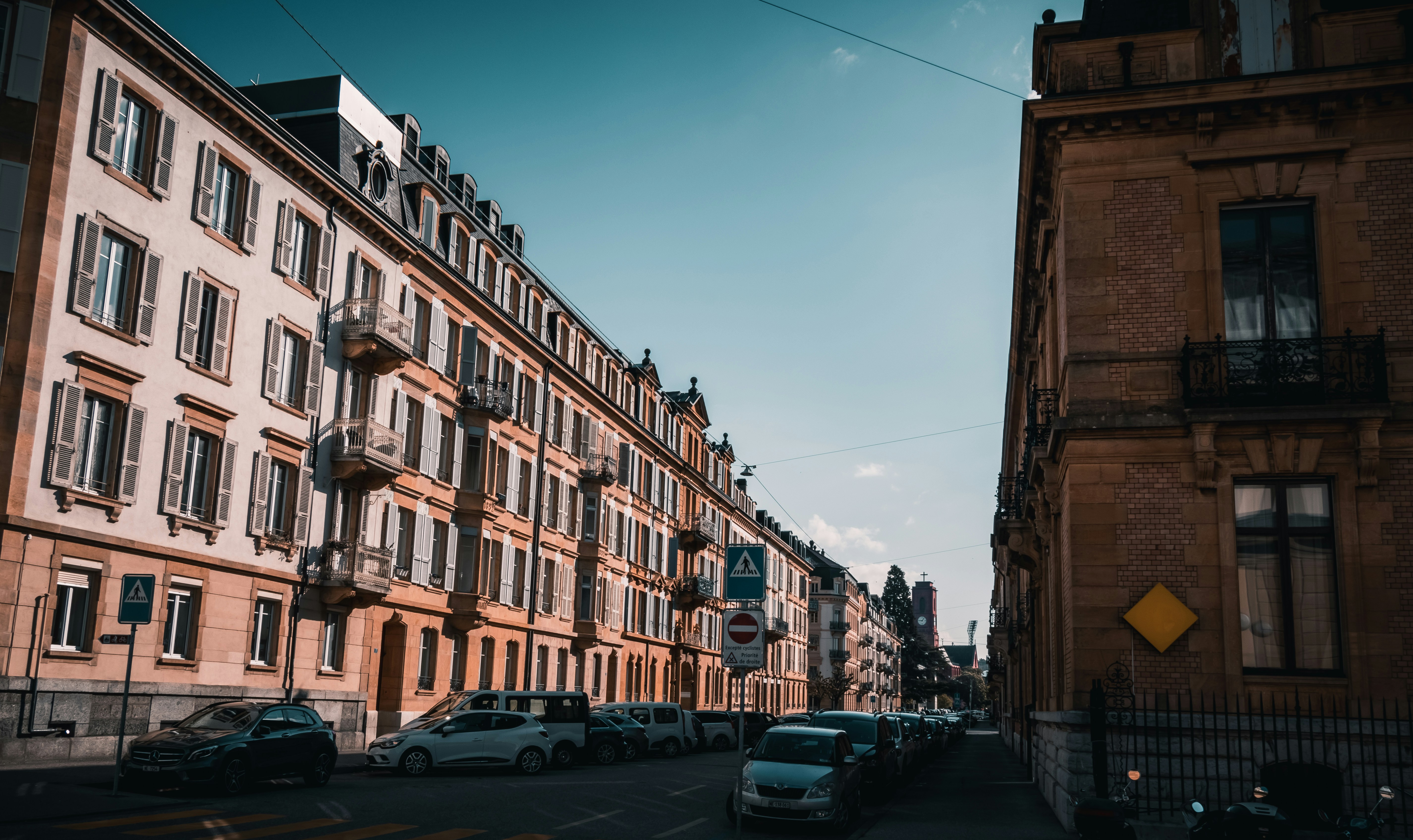 Charming street scene showcasing classic architecture and parked cars along a sunlit avenue. The buildings exhibit a blend of historical and modern design elements.