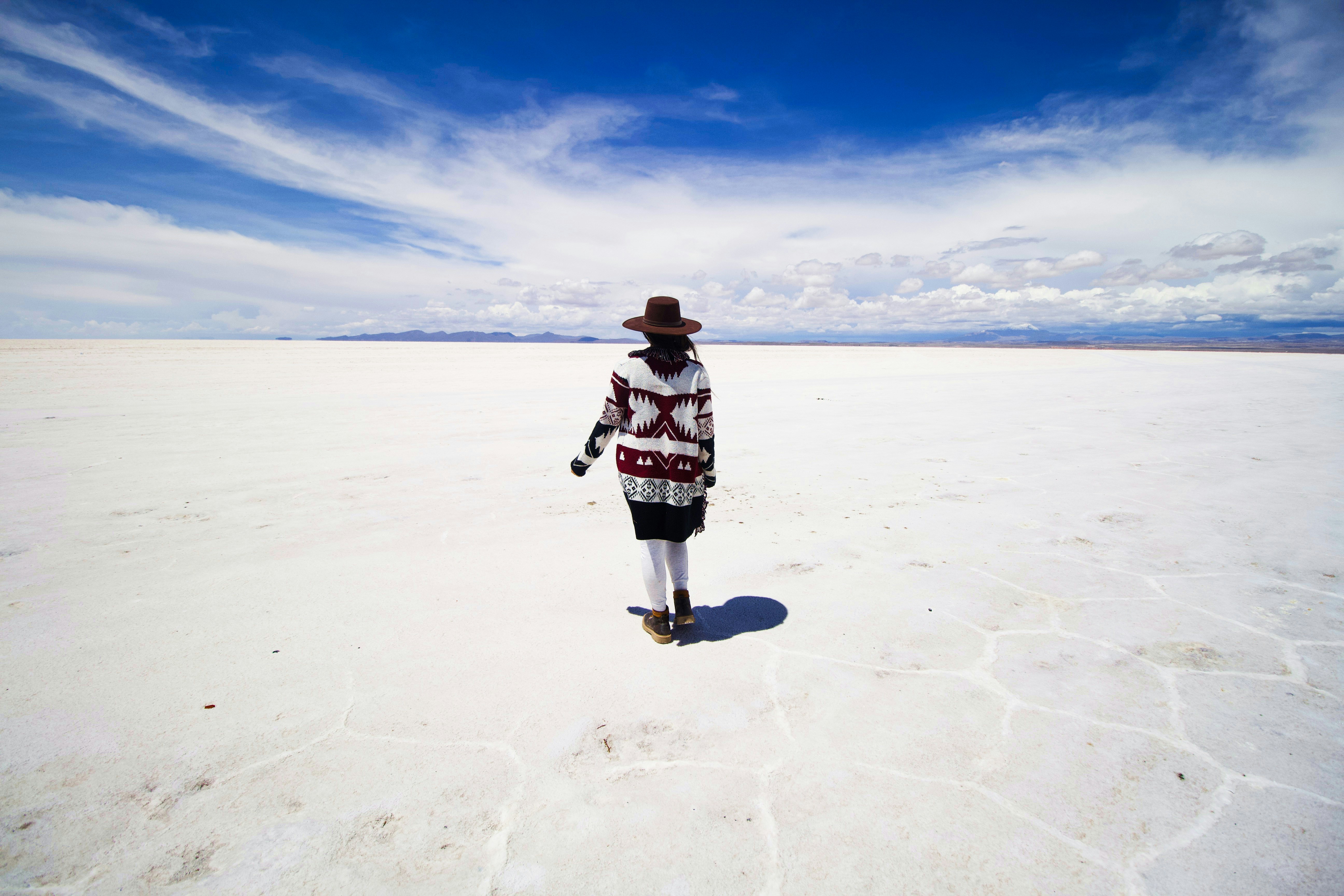 Person in a patterned sweater and hat walking on vast white salt flats under a blue sky.
