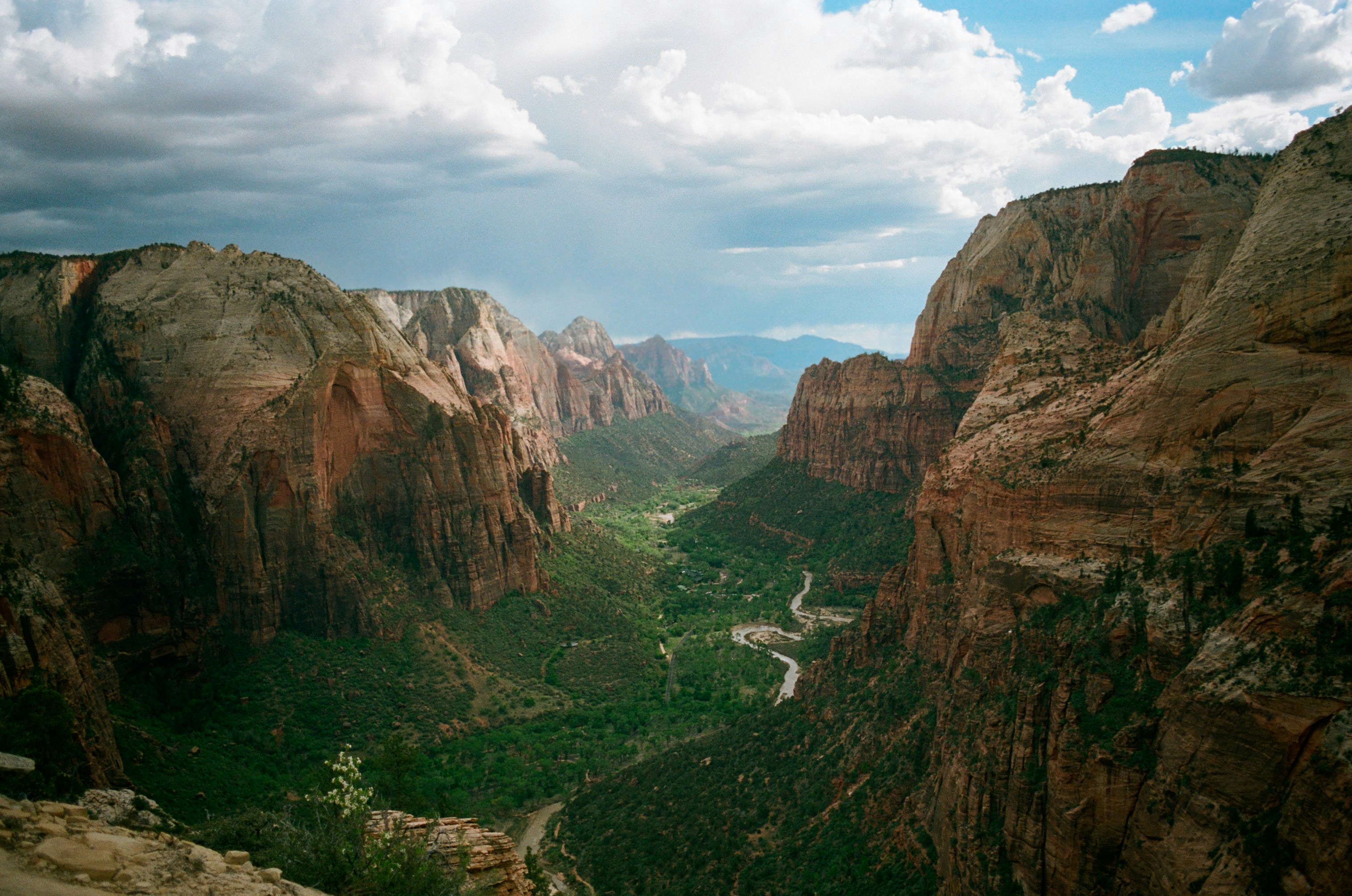 Vast canyon landscape showcasing towering red cliffs and a winding river below, illuminated by dramatic cloud formations. 