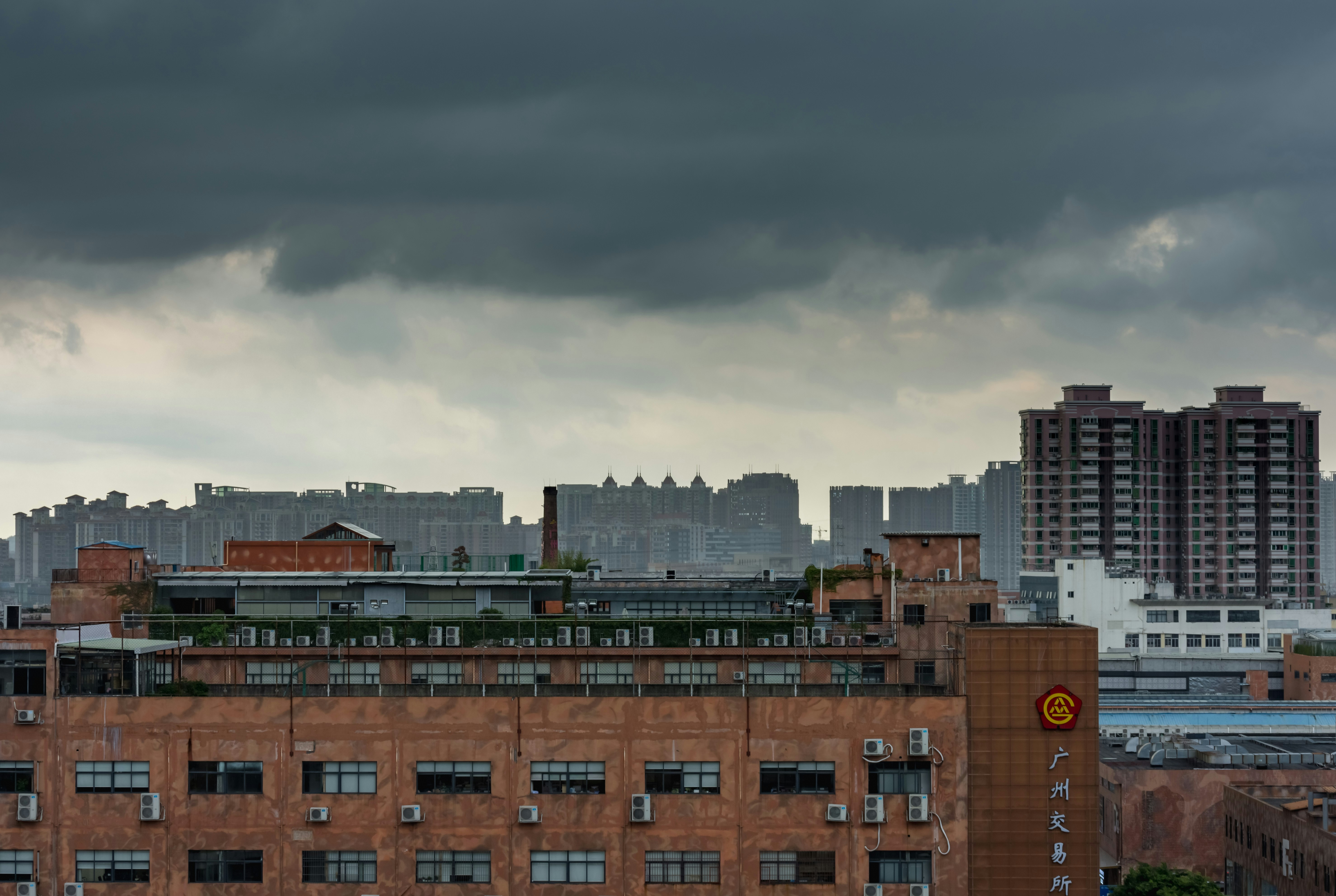 Brick industrial building set against a backdrop of dark storm clouds and a city skyline.