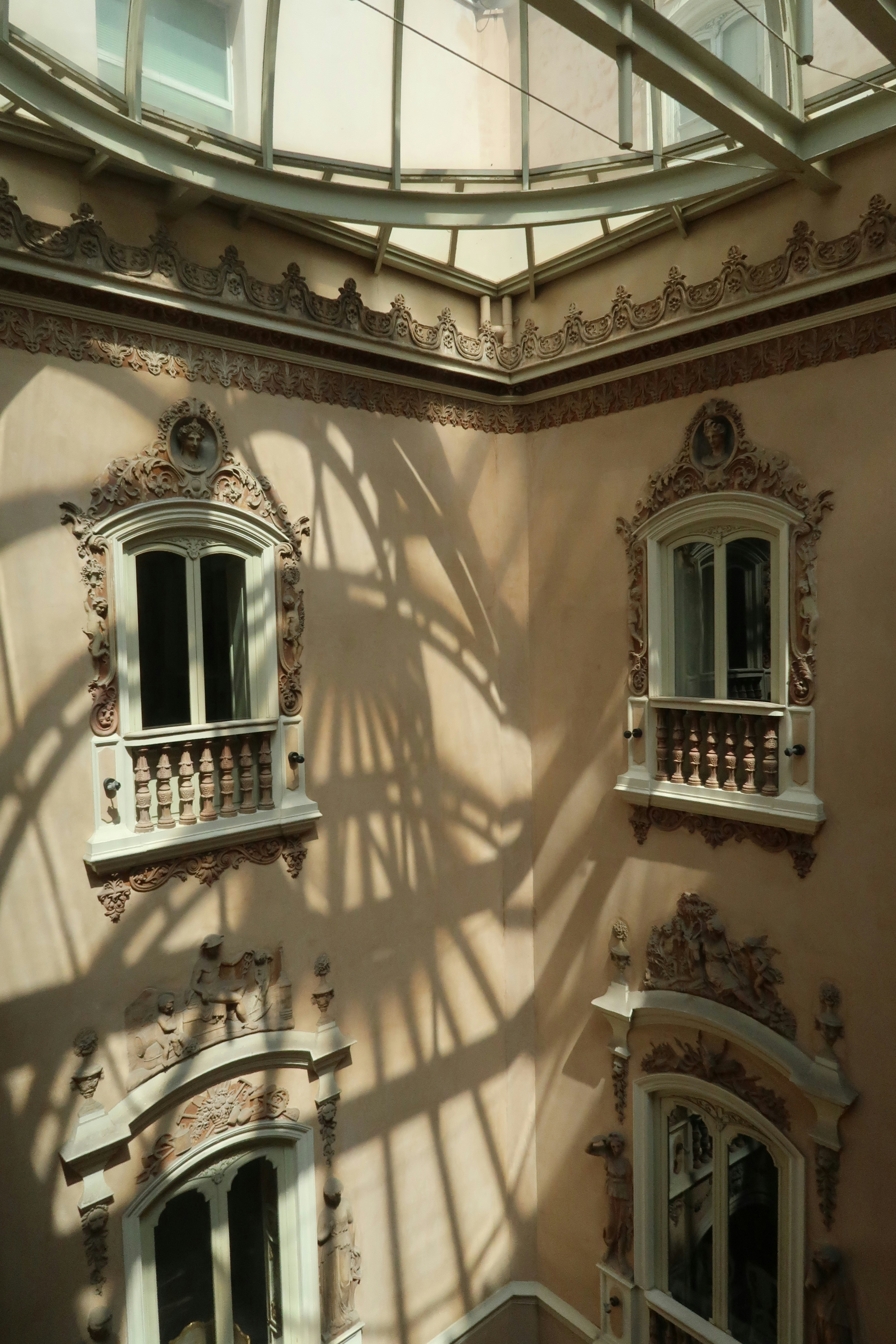 Lattice Shadows on a Peach Facade: Ornate Windows in a Sunlit Courtyard