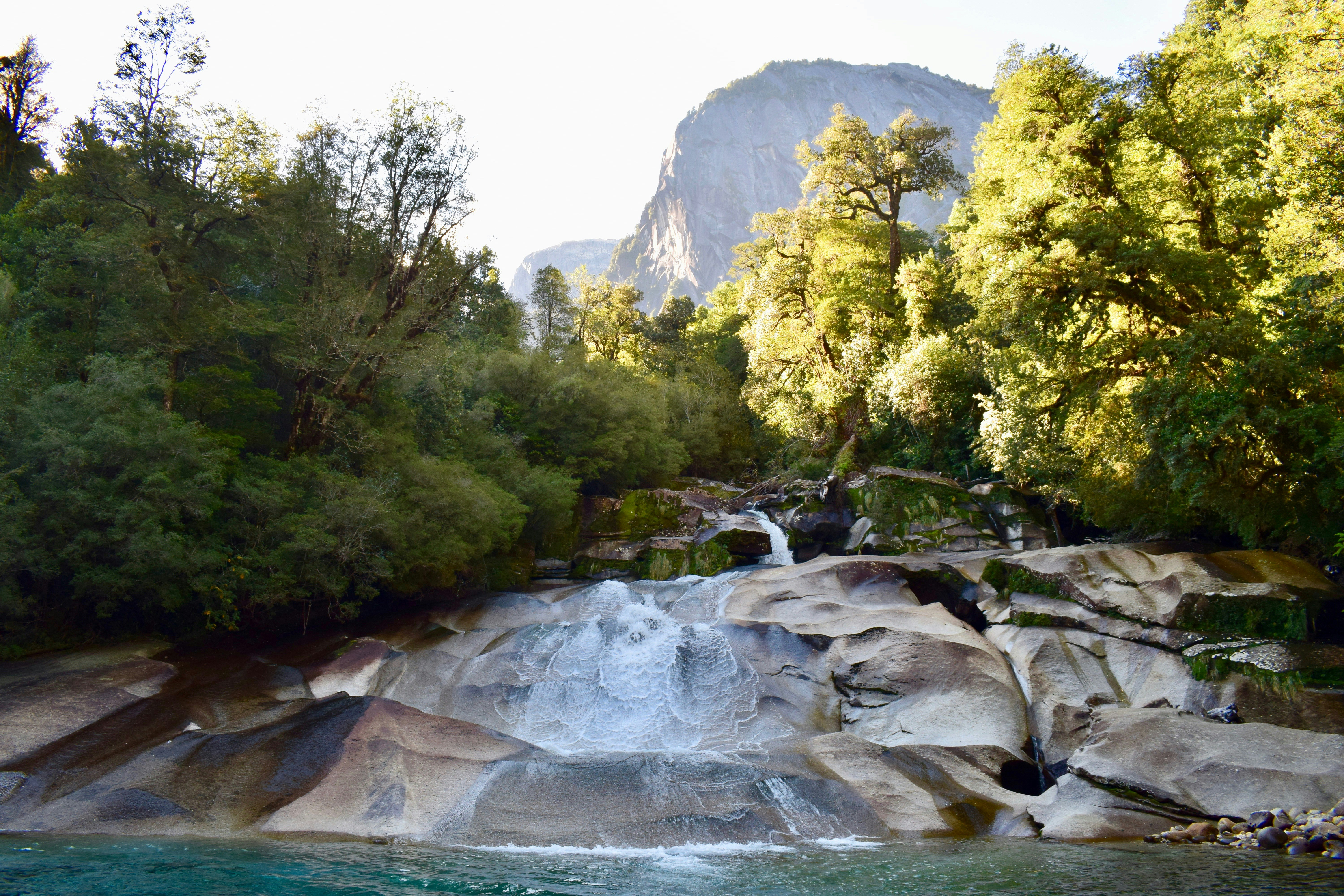 Gentle waterfall cascading over smooth rocks, surrounded by lush greenery and towering cliffs. The scene captures the tranquil essence of a natural oasis.